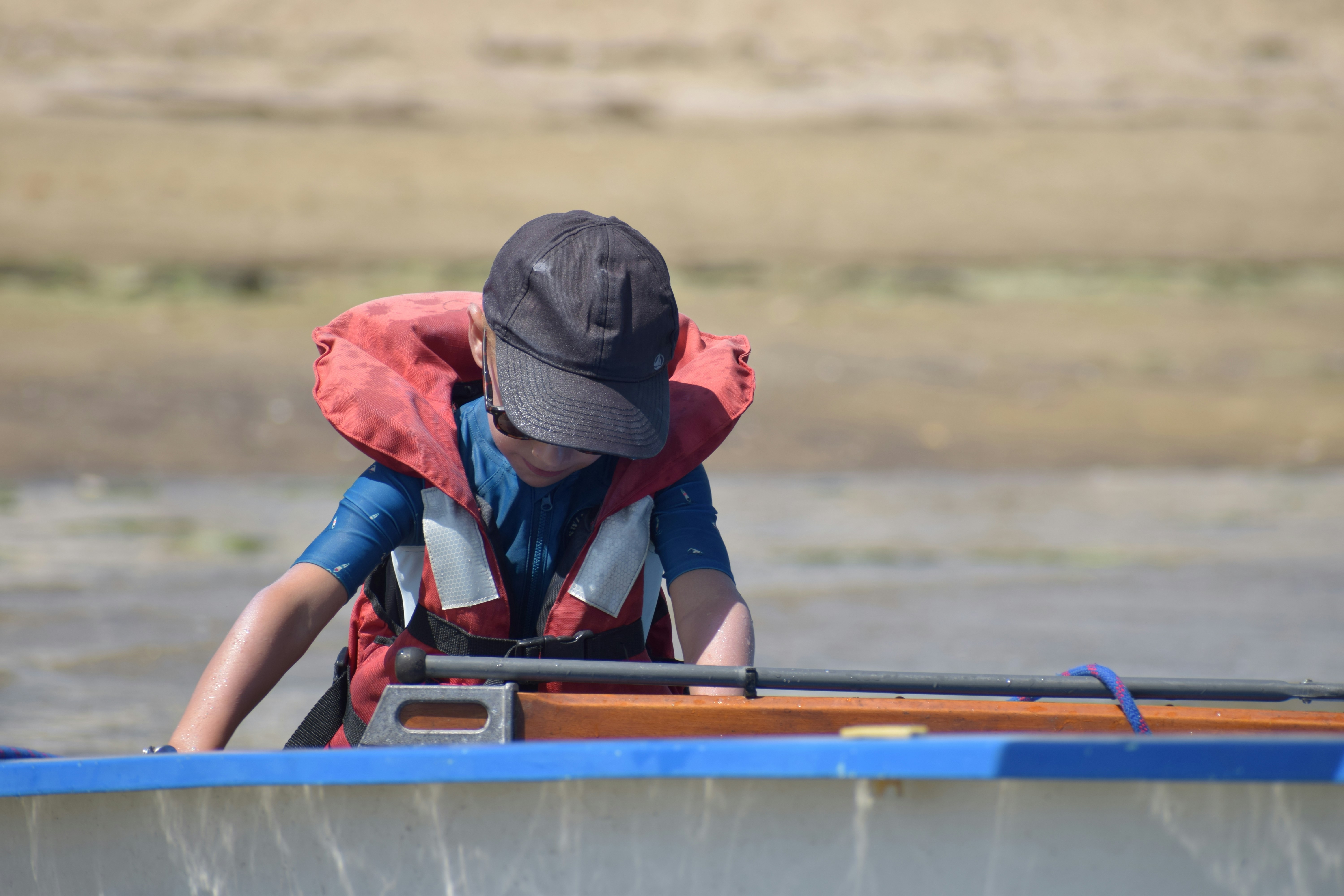 Child in a life vest at the bow of a small boat on a calm shoreline