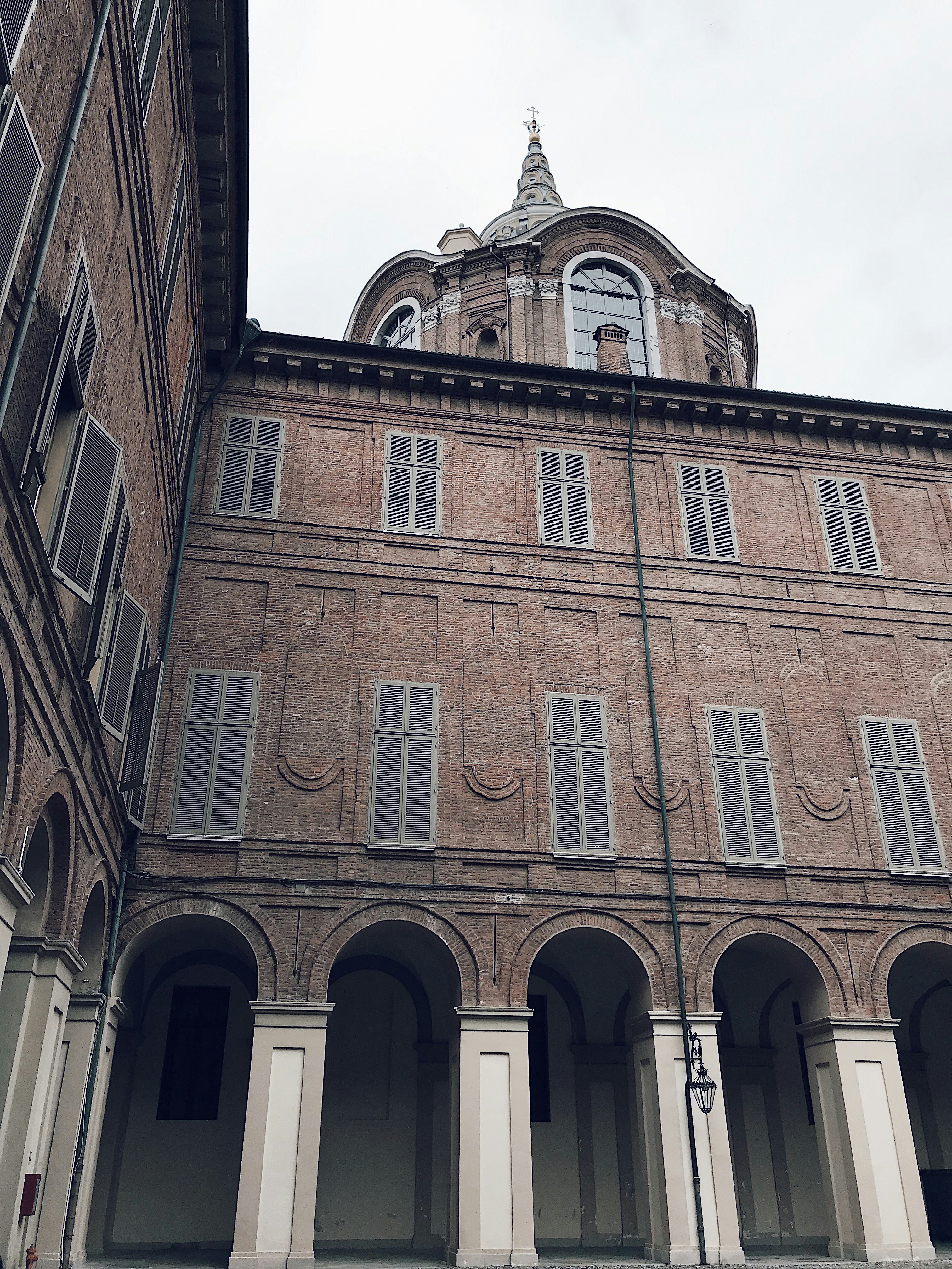 Historic building with arched colonnade and intricate dome under a cloudy sky.