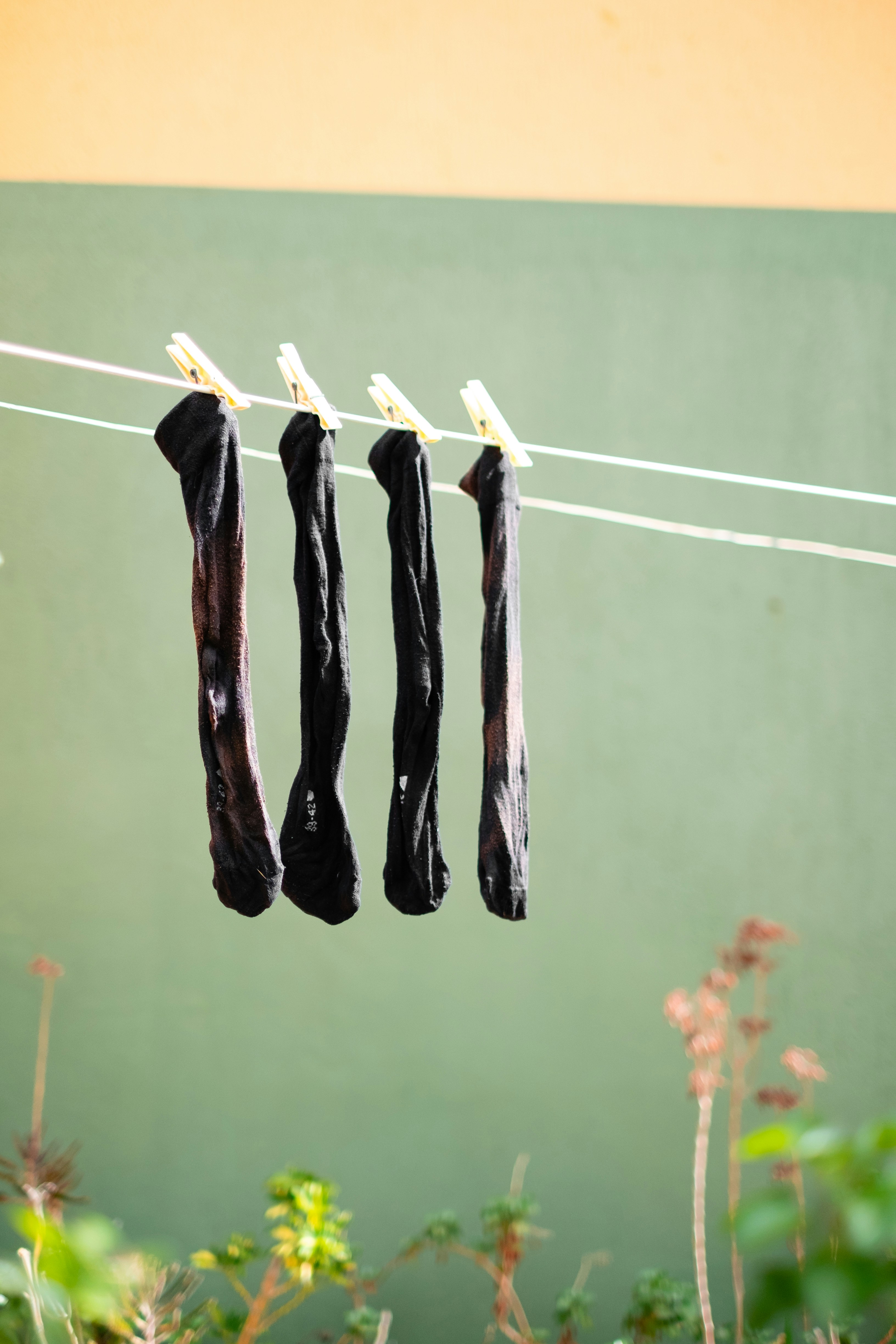 Four dark fabric strips hang from a clothesline against a pastel green wall, their wrinkled texture catching the soft daylight.