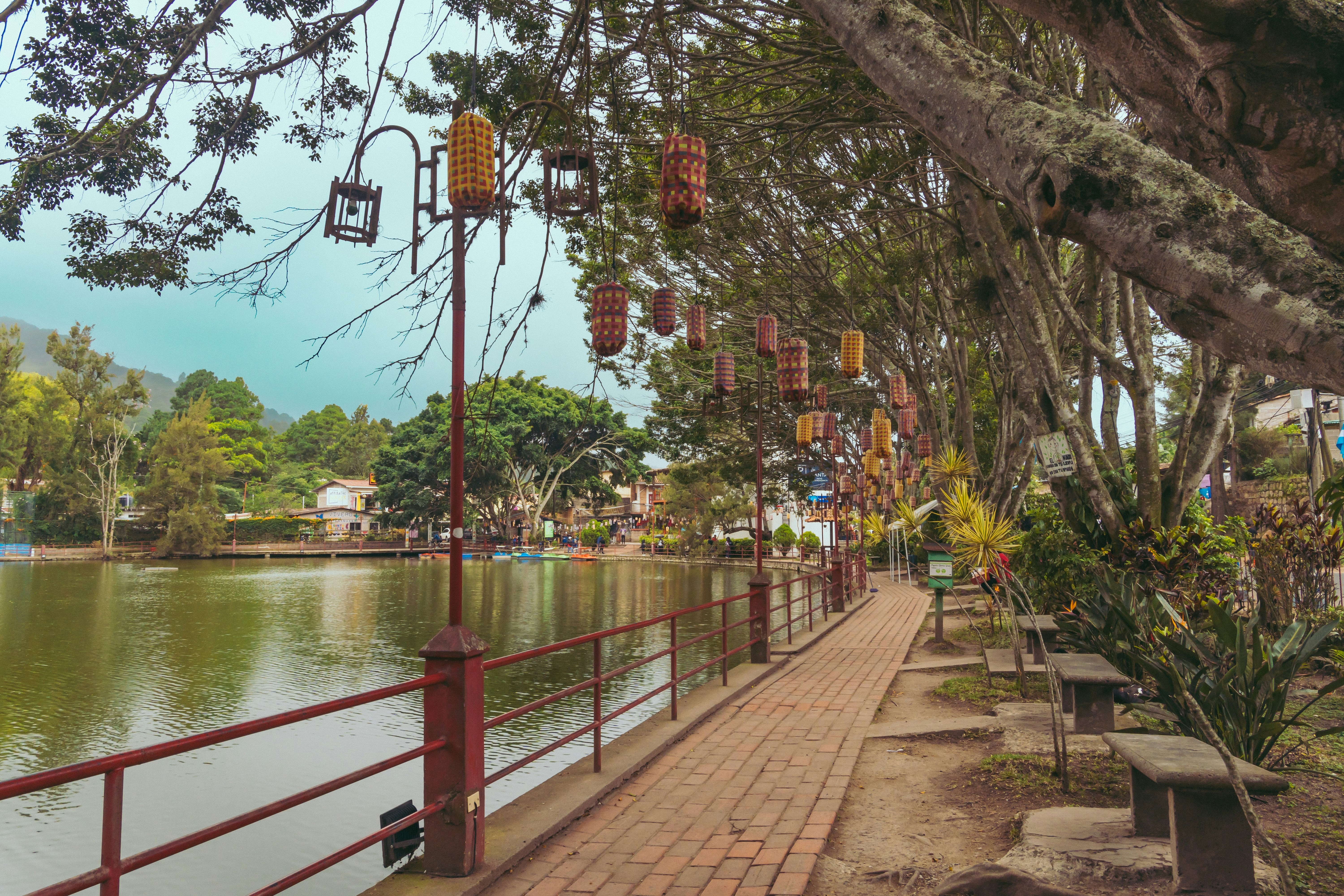 Brick pathway lined with lanterns and trees alongside a tranquil river.
