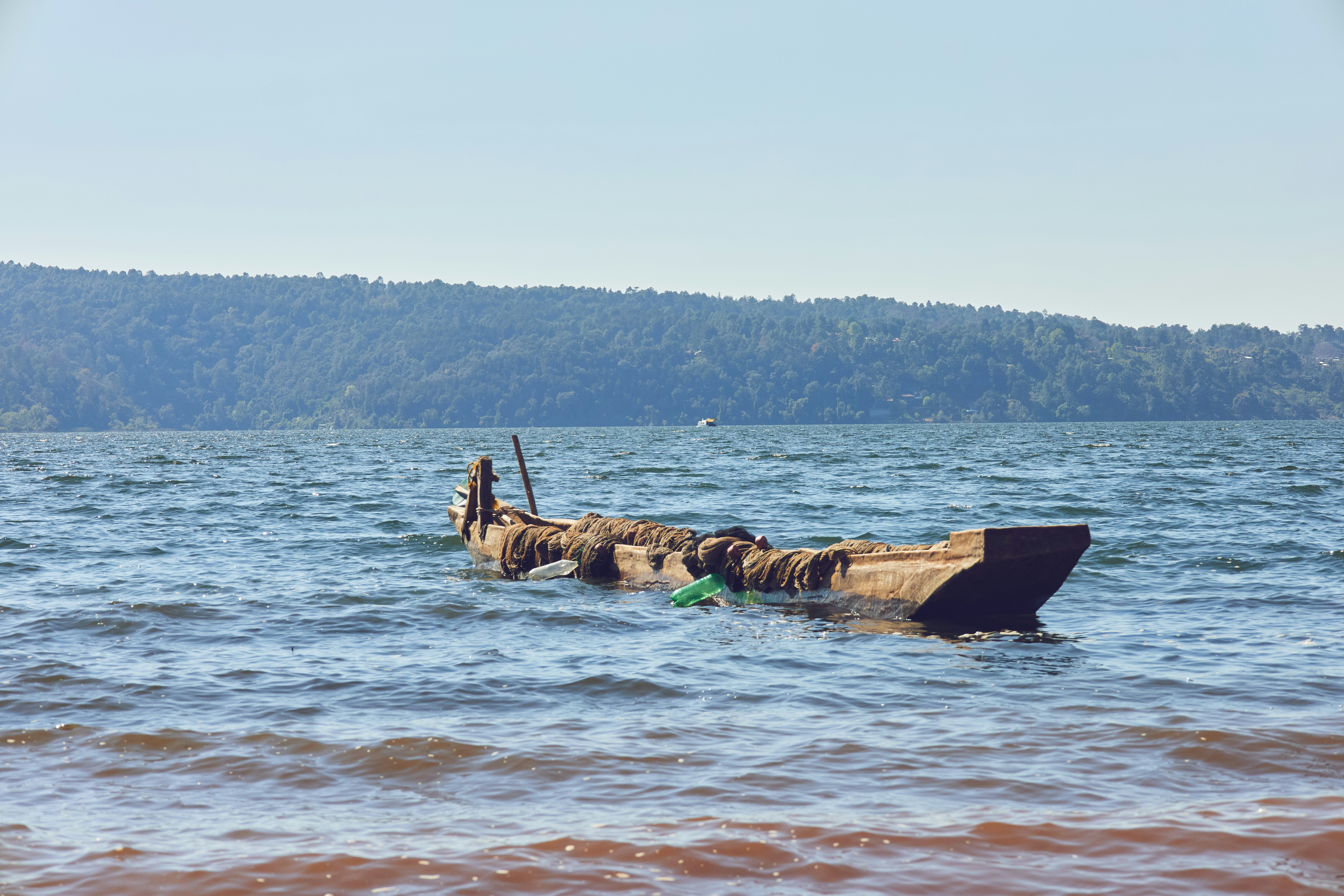 Partially submerged wooden boat floating on a serene lake with forested hills in the background.