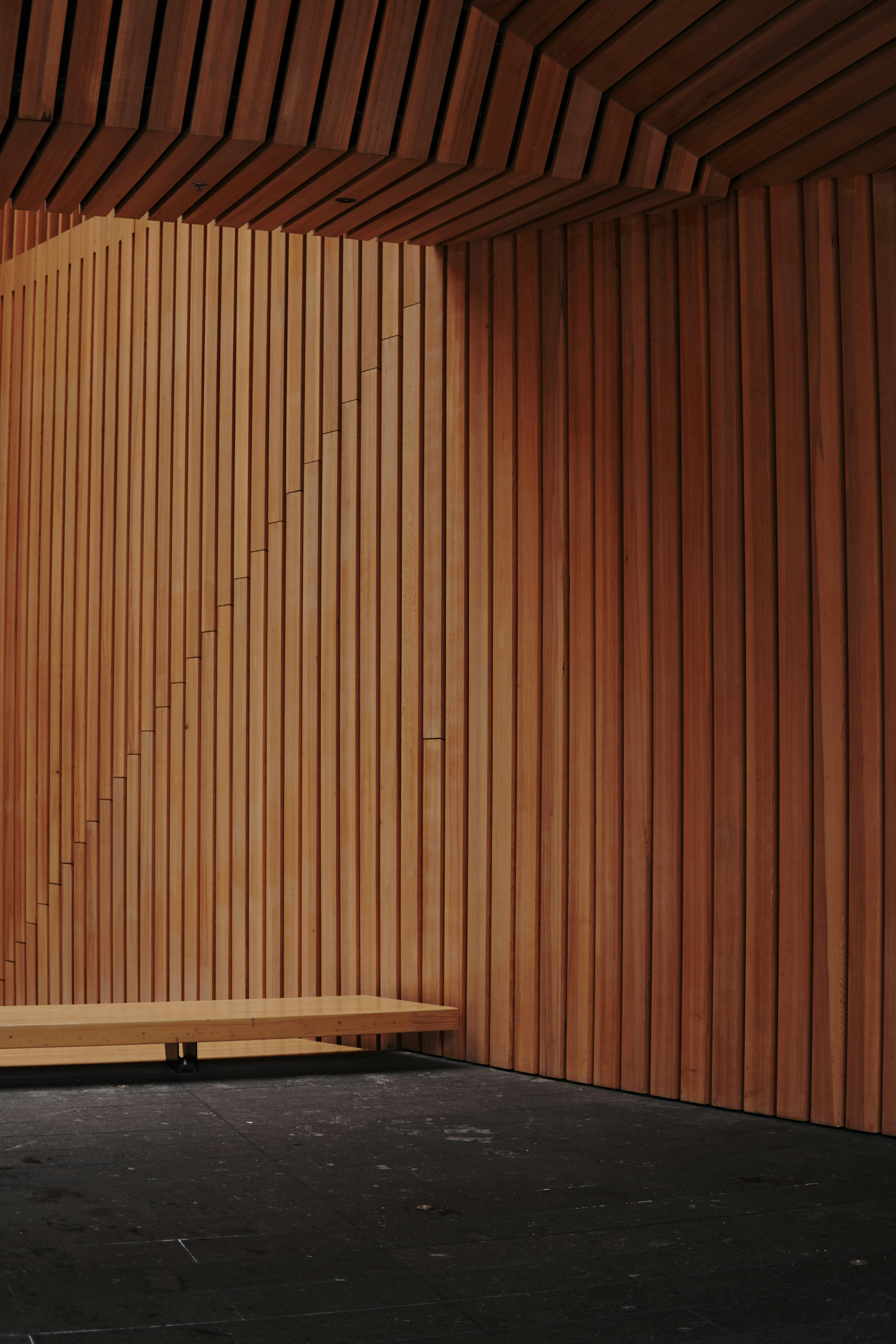 Minimalist architecture with vertical wooden slats casting geometric shadows on a dark floor.