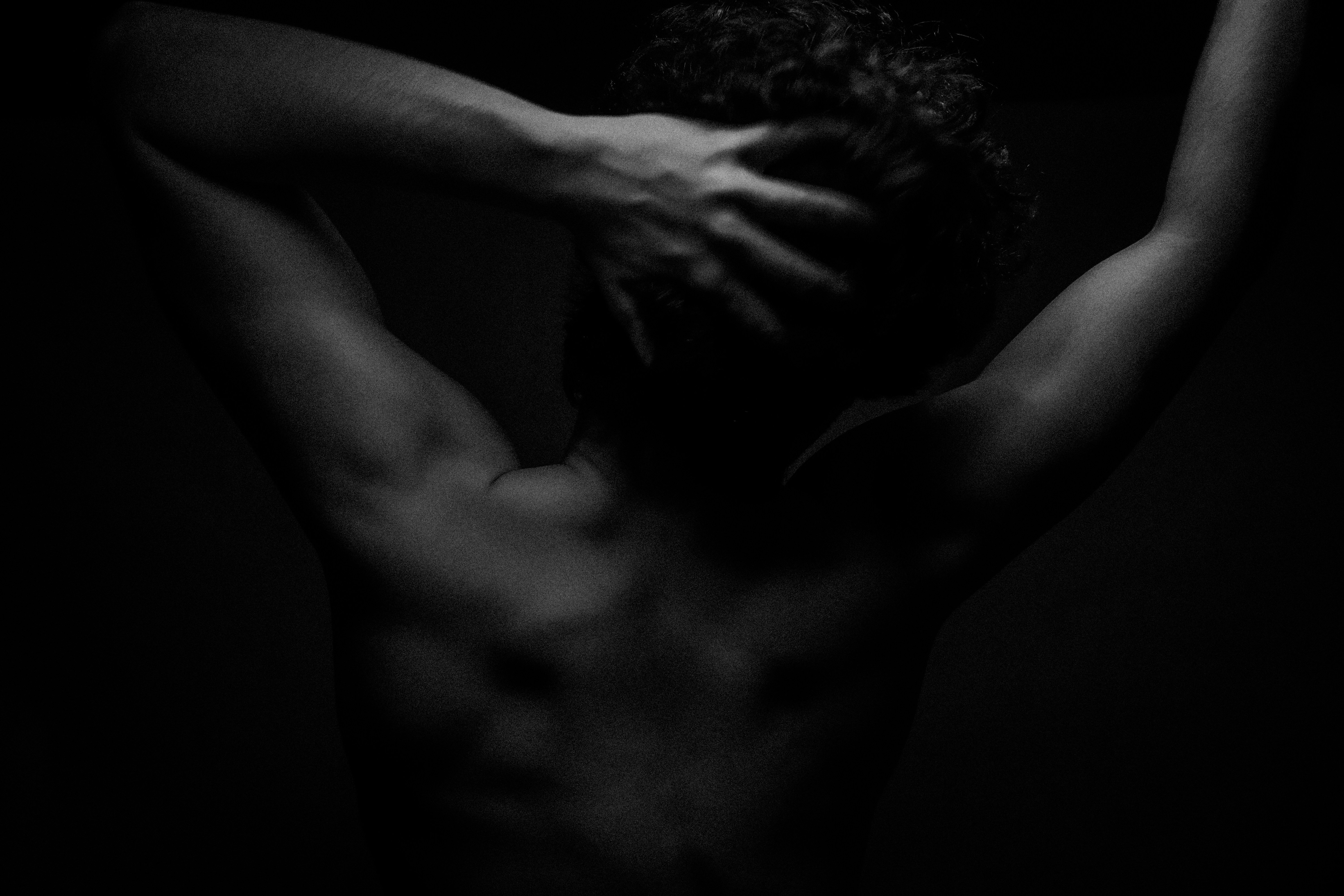 A figure with curly hair, viewed from behind, grips their head in a moment of introspection against a dark backdrop.