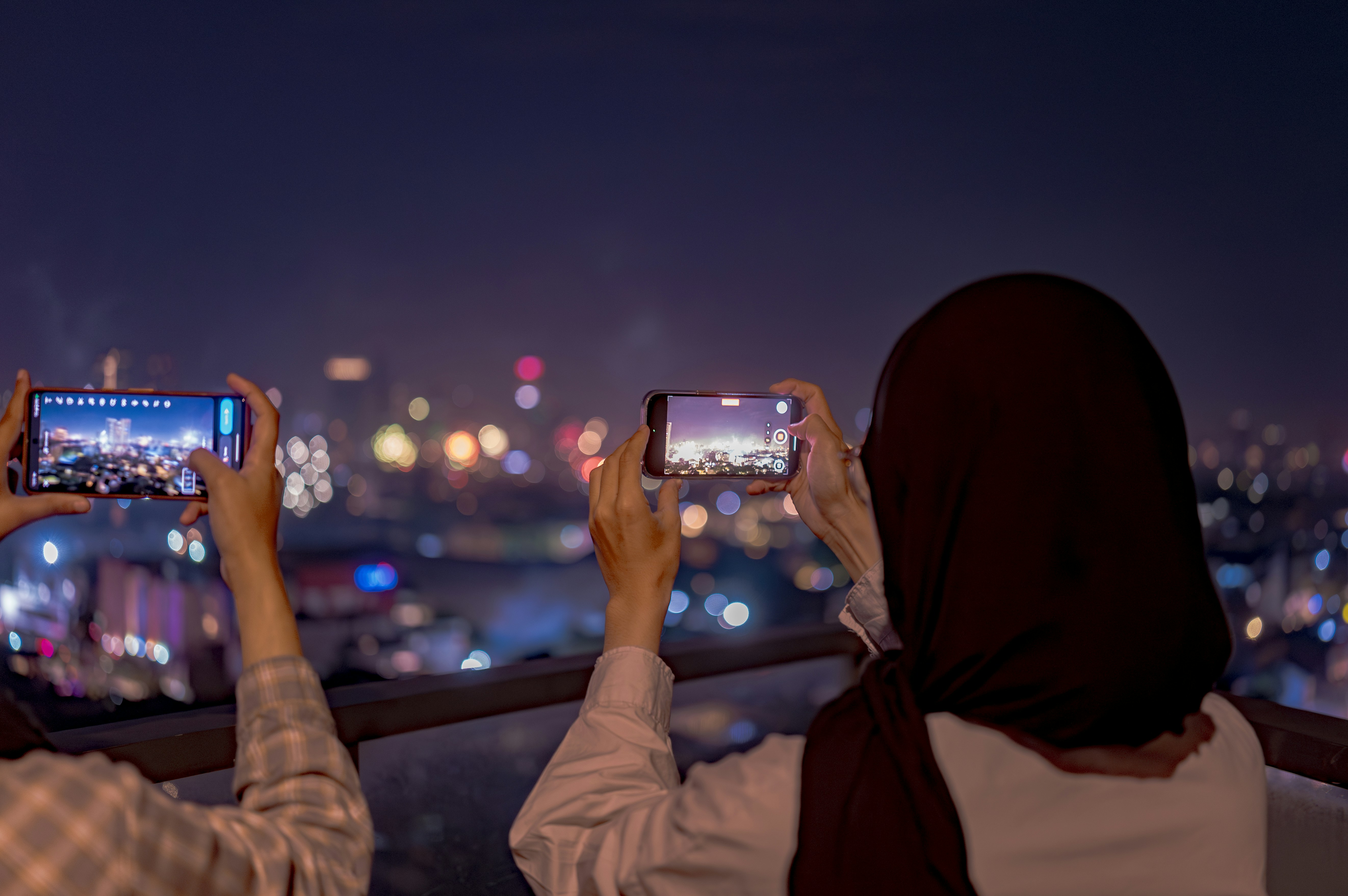 Two people taking pictures of a city at night photo – Free Jakarta ...