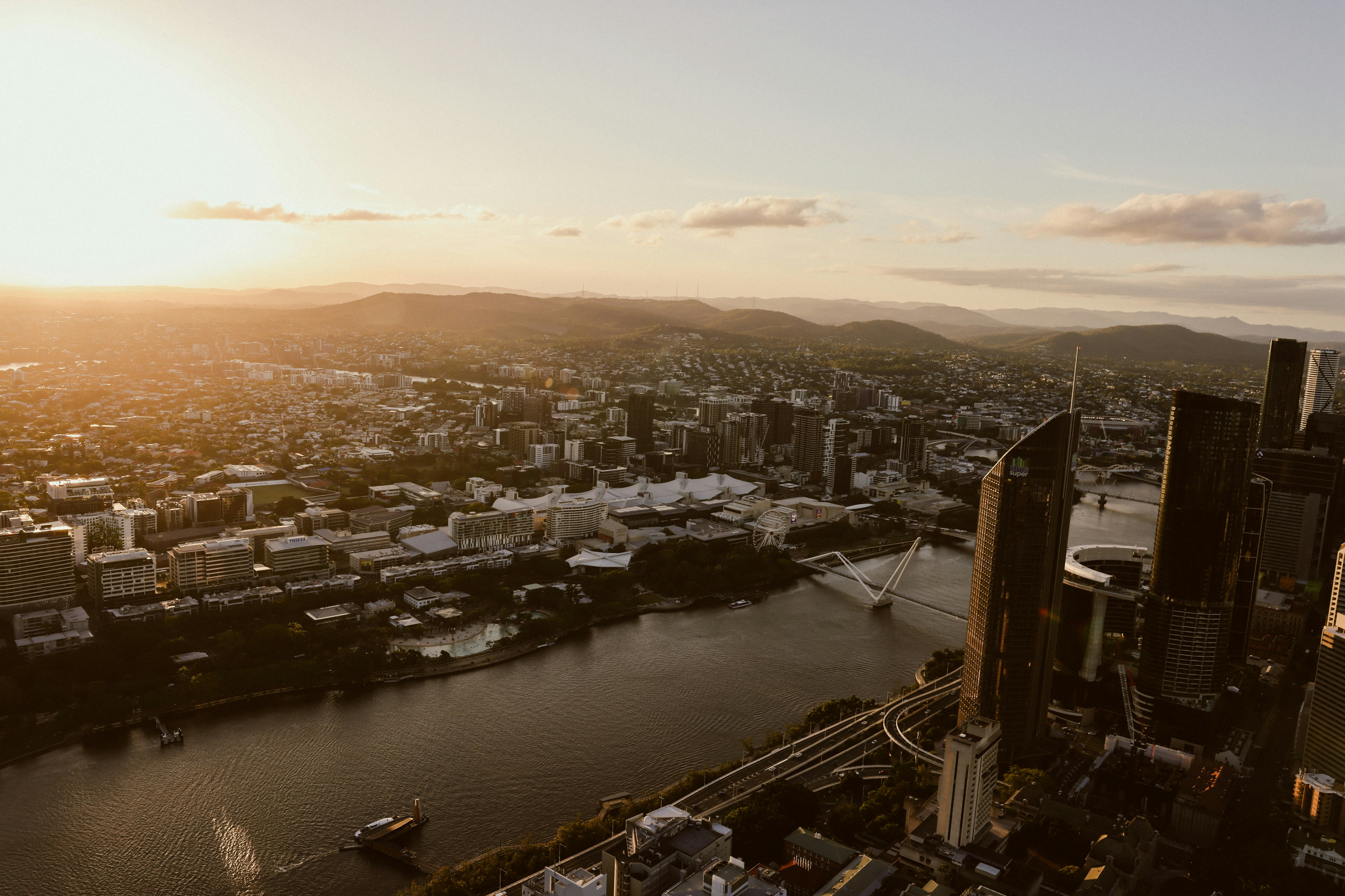 Aerial view of Brisbane city at sunset with the river winding through tall skyscrapers and South Bank.