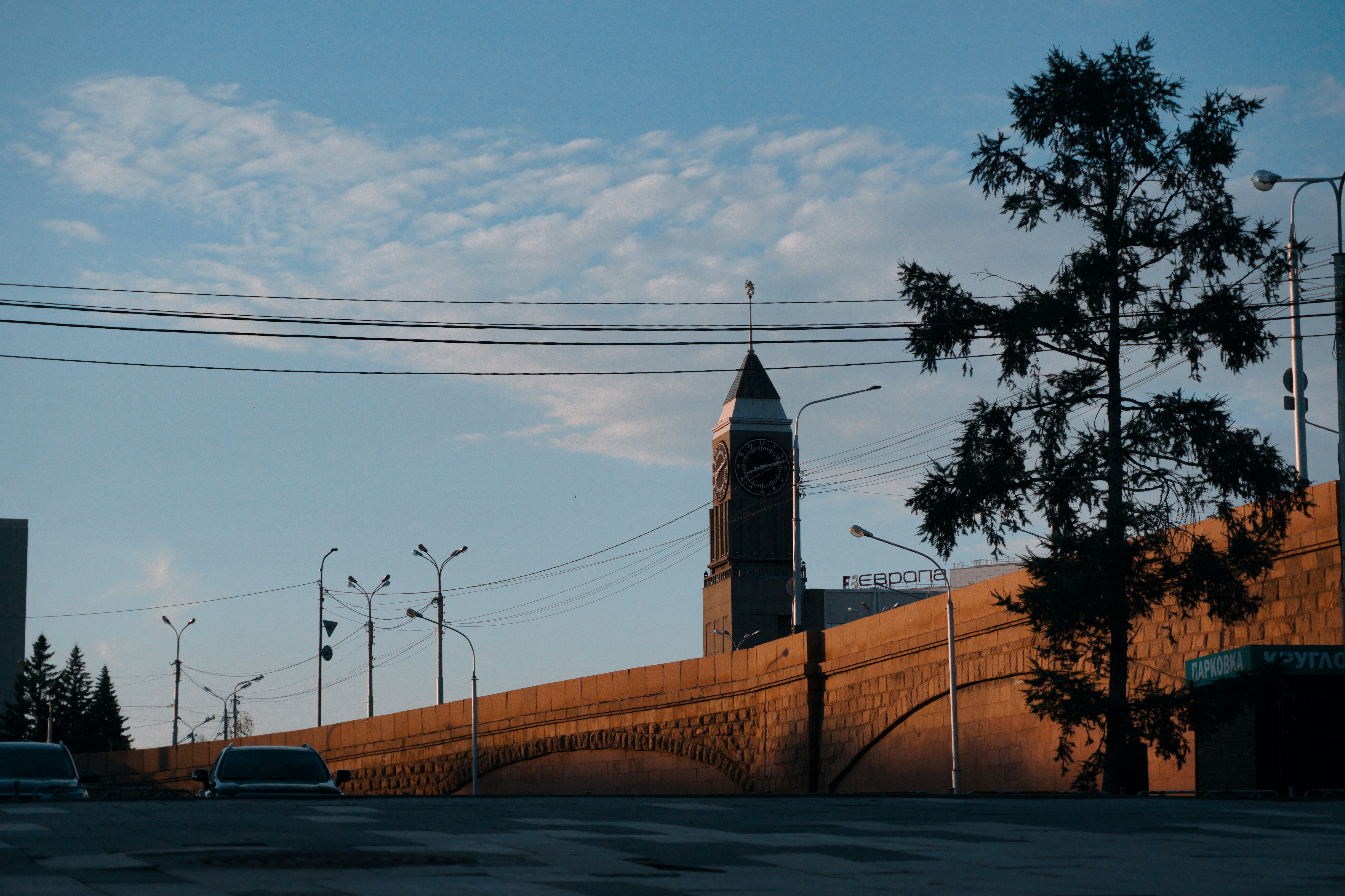 Clock tower rising above a gently sloping brick wall under a soft evening sky.