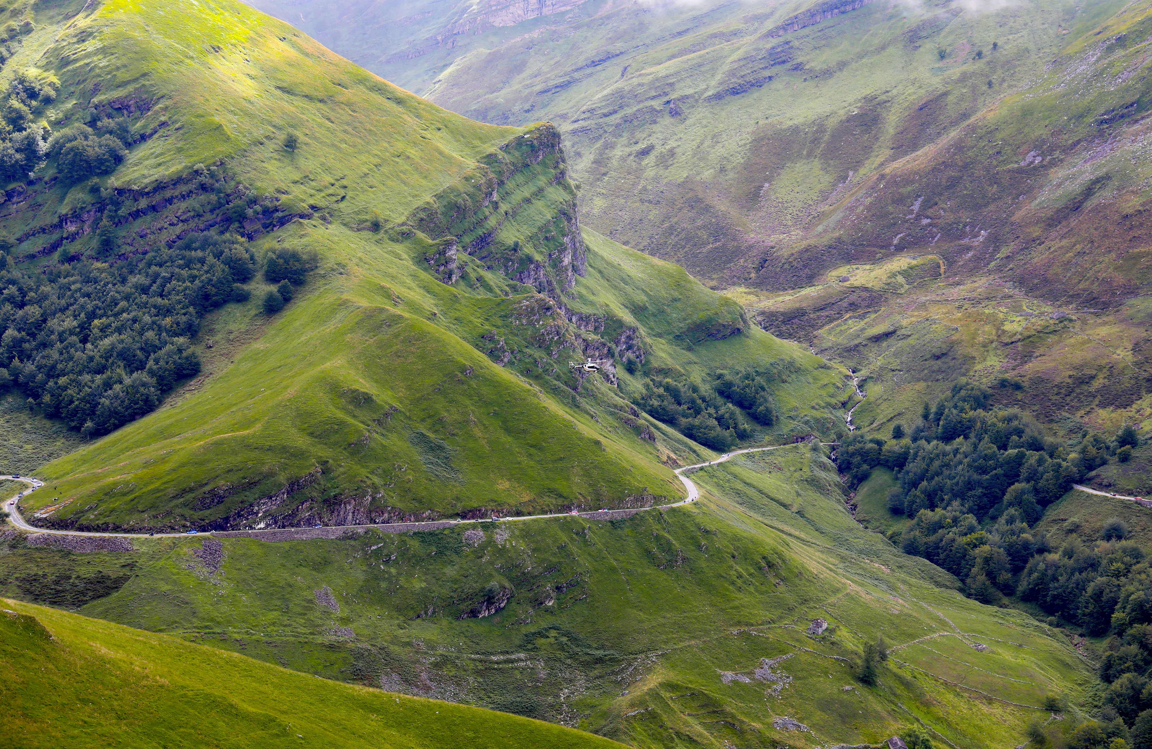 Cyclists navigate a winding road through lush green mountains, showcasing both athleticism and nature's beauty.