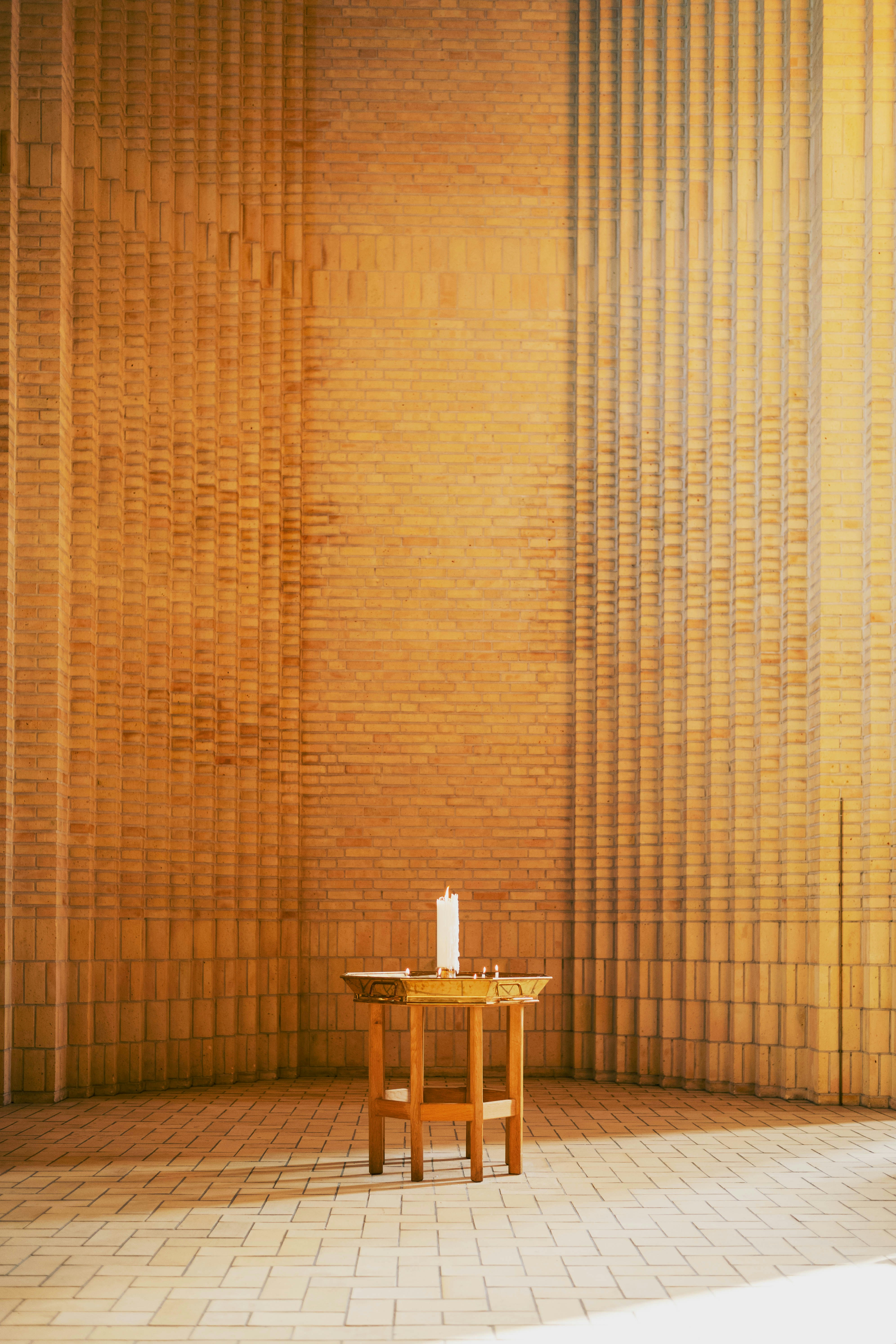 Wooden table with a lit candle against warm, textured brick walls emphasizing vertical symmetry.
