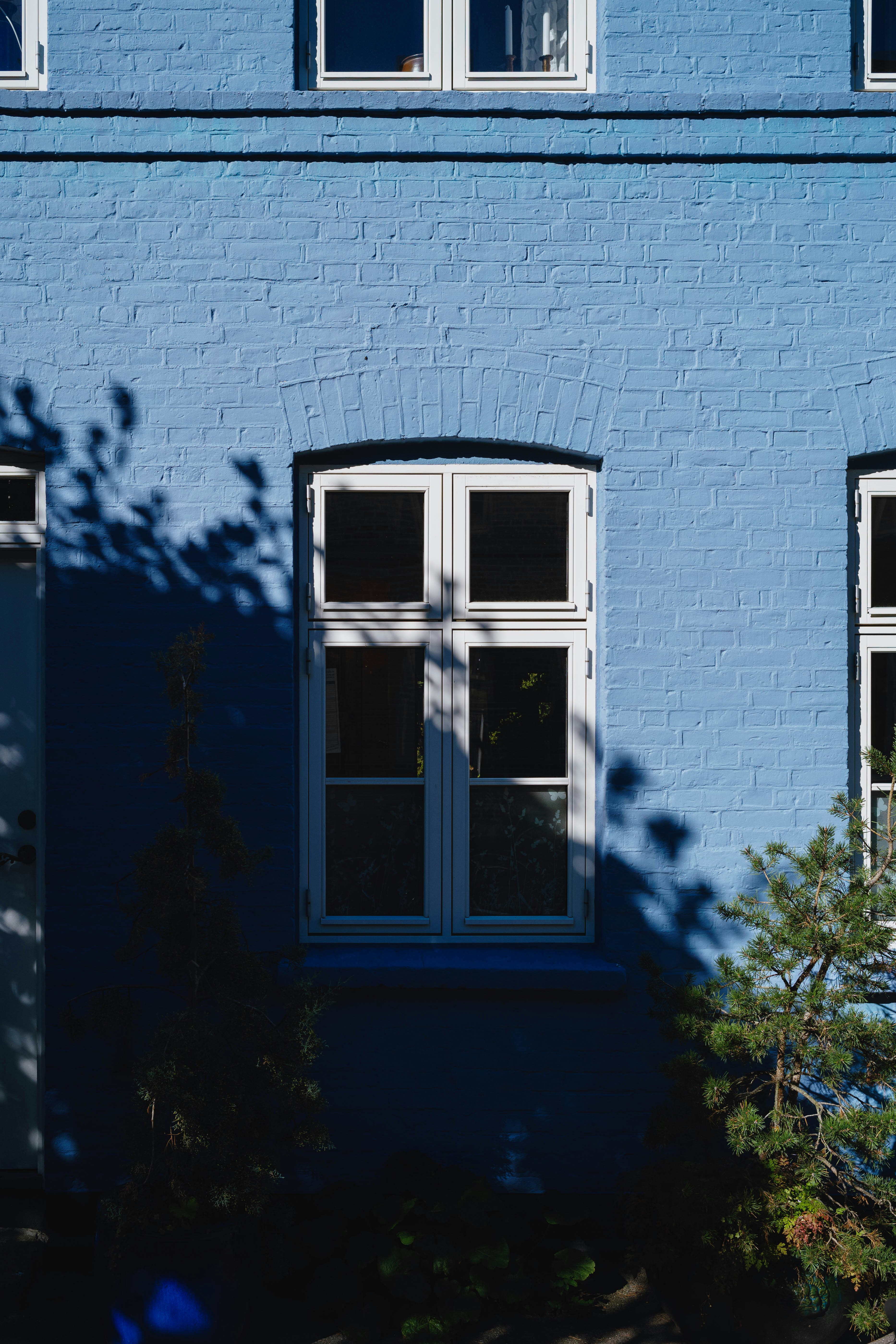 Vibrant blue facade with white-framed windows, casting intricate shadows that create depth and a serene atmosphere.
