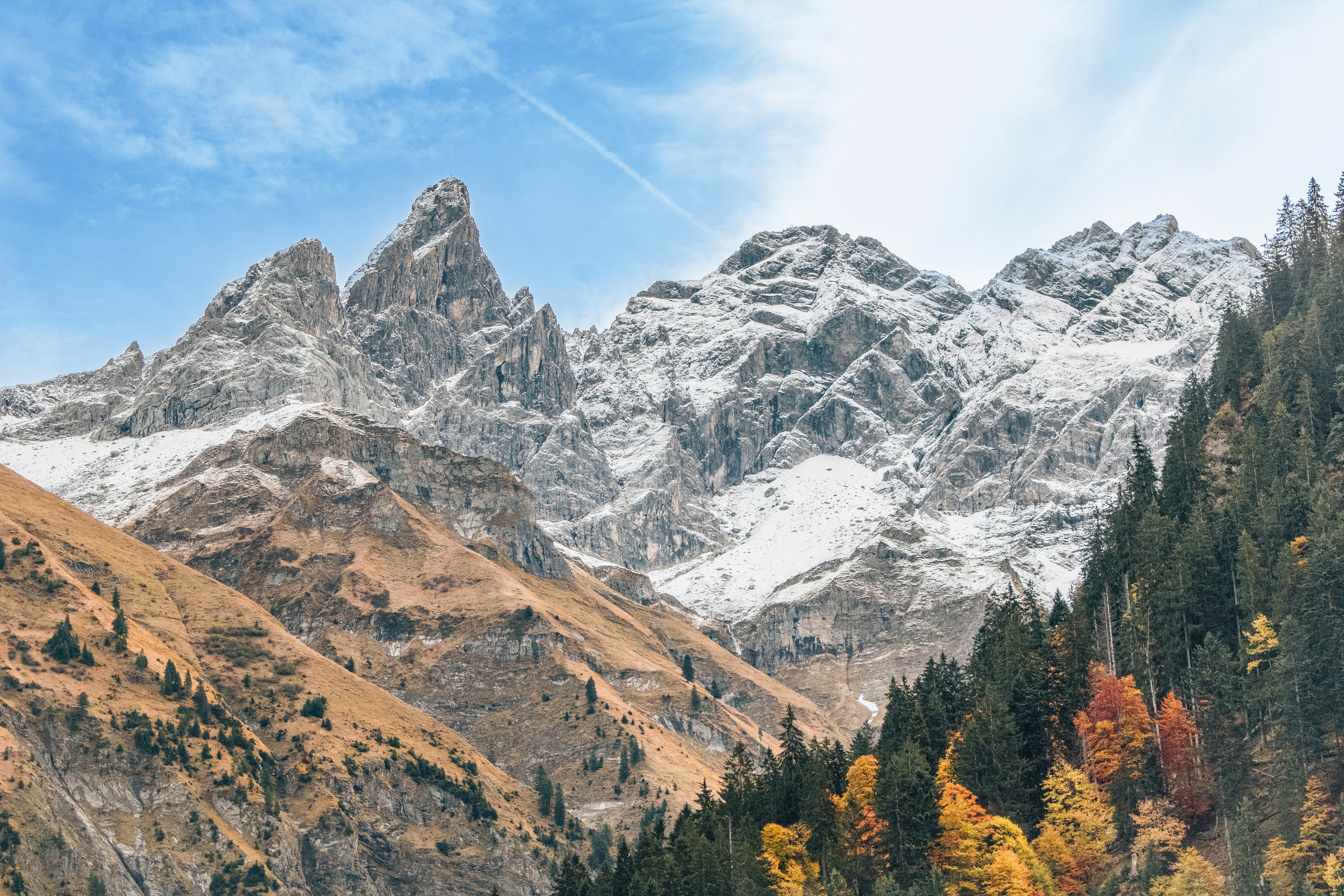 Majestic mountain range adorned with a dusting of snow, surrounded by vibrant autumn foliage in the foreground.