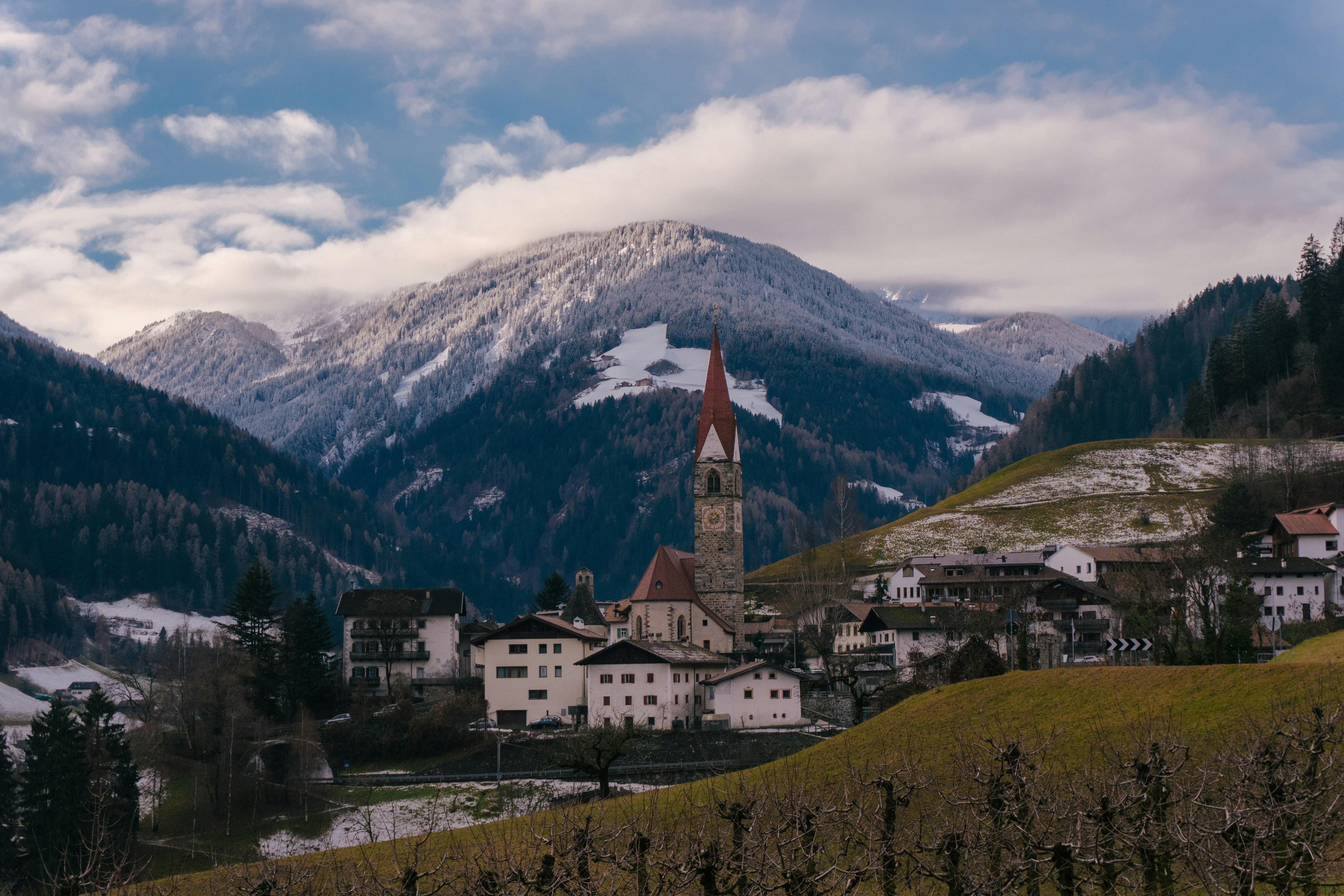 Charming village nestled against snow-capped mountains under a partly cloudy sky.