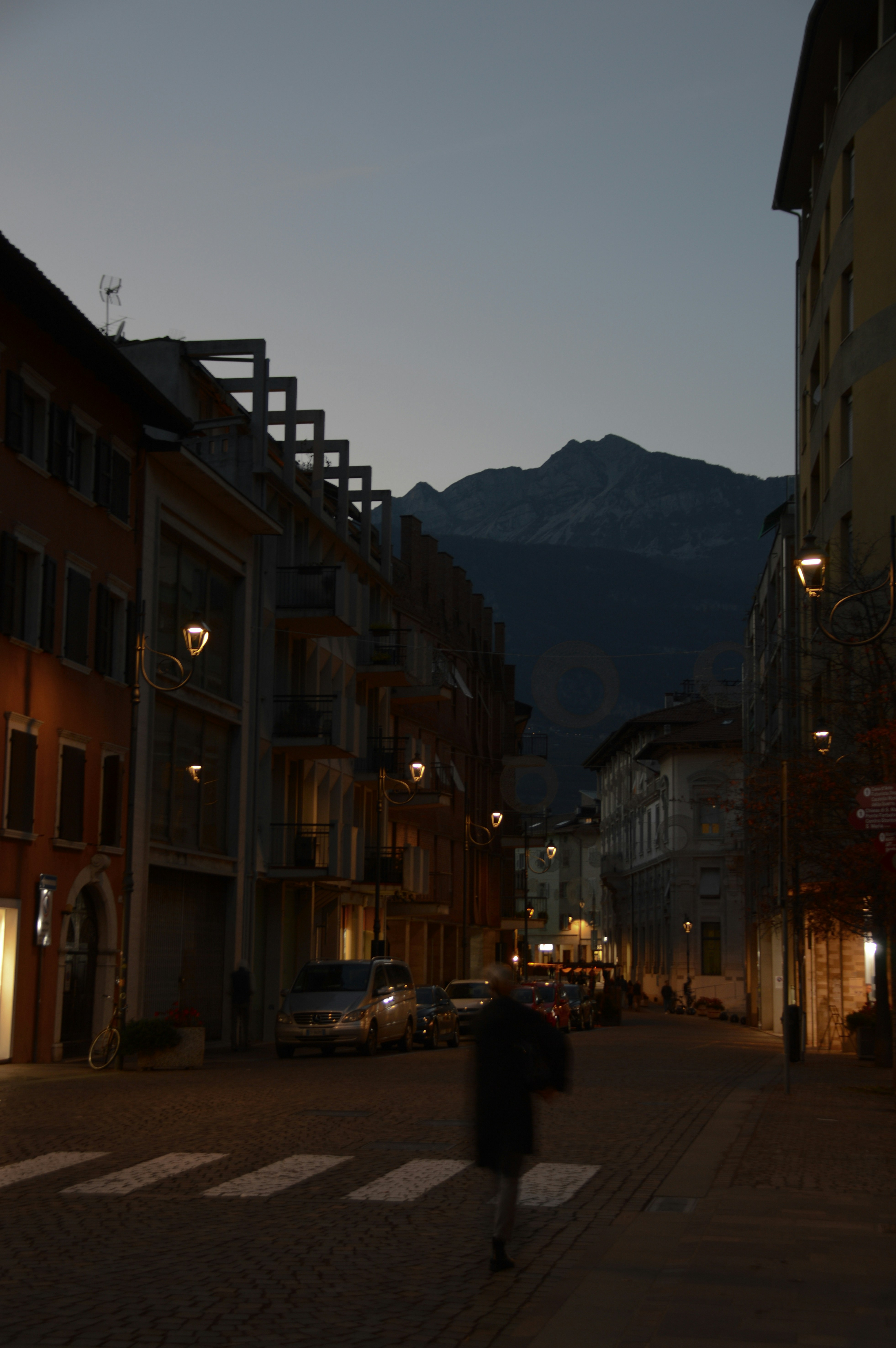 Dimly lit street at dusk with mountains in the background and a solitary person walking.