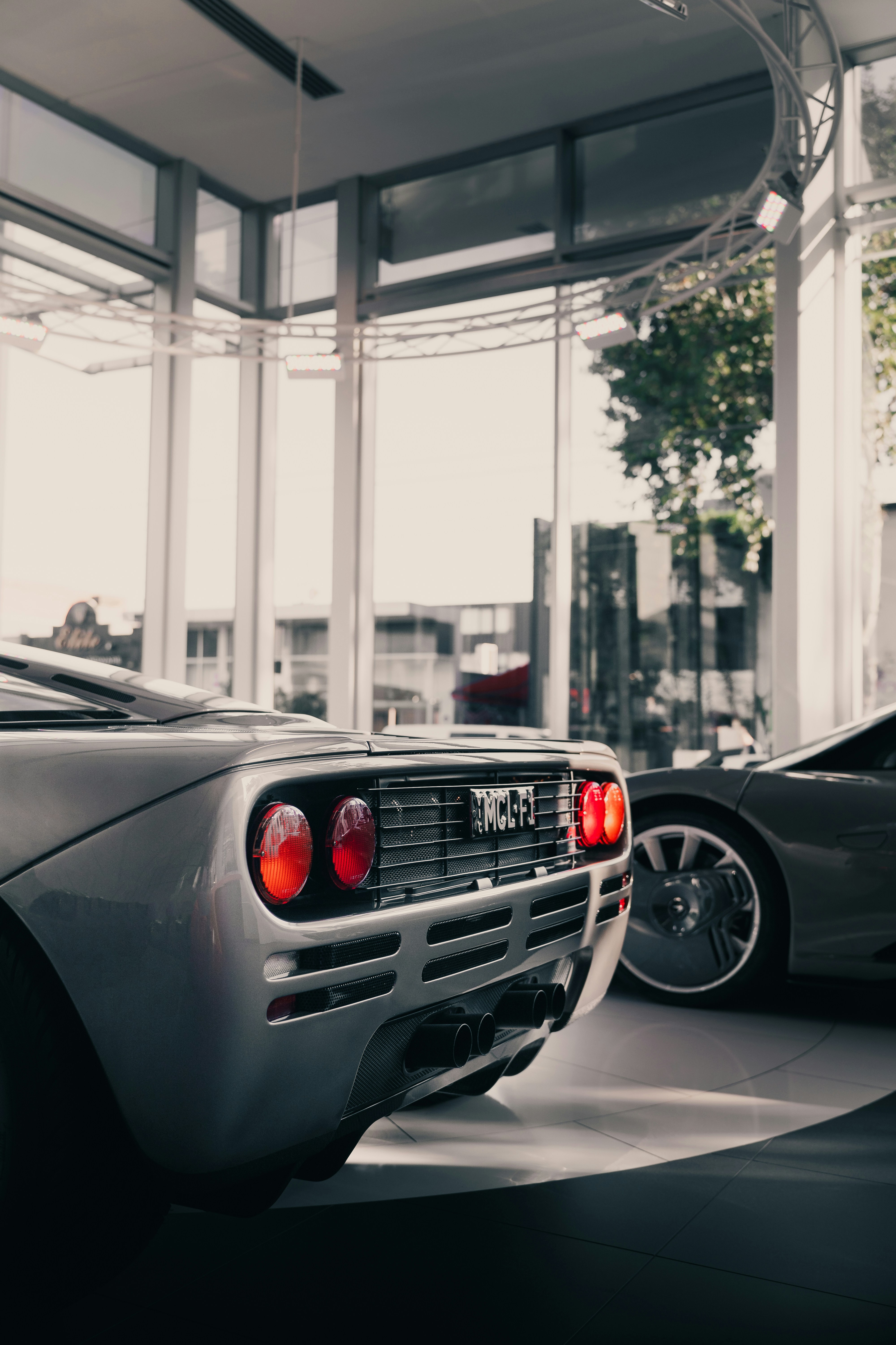 Tail-Light Reverie: A Silver Sports Car in a Glass-Washed Showroom