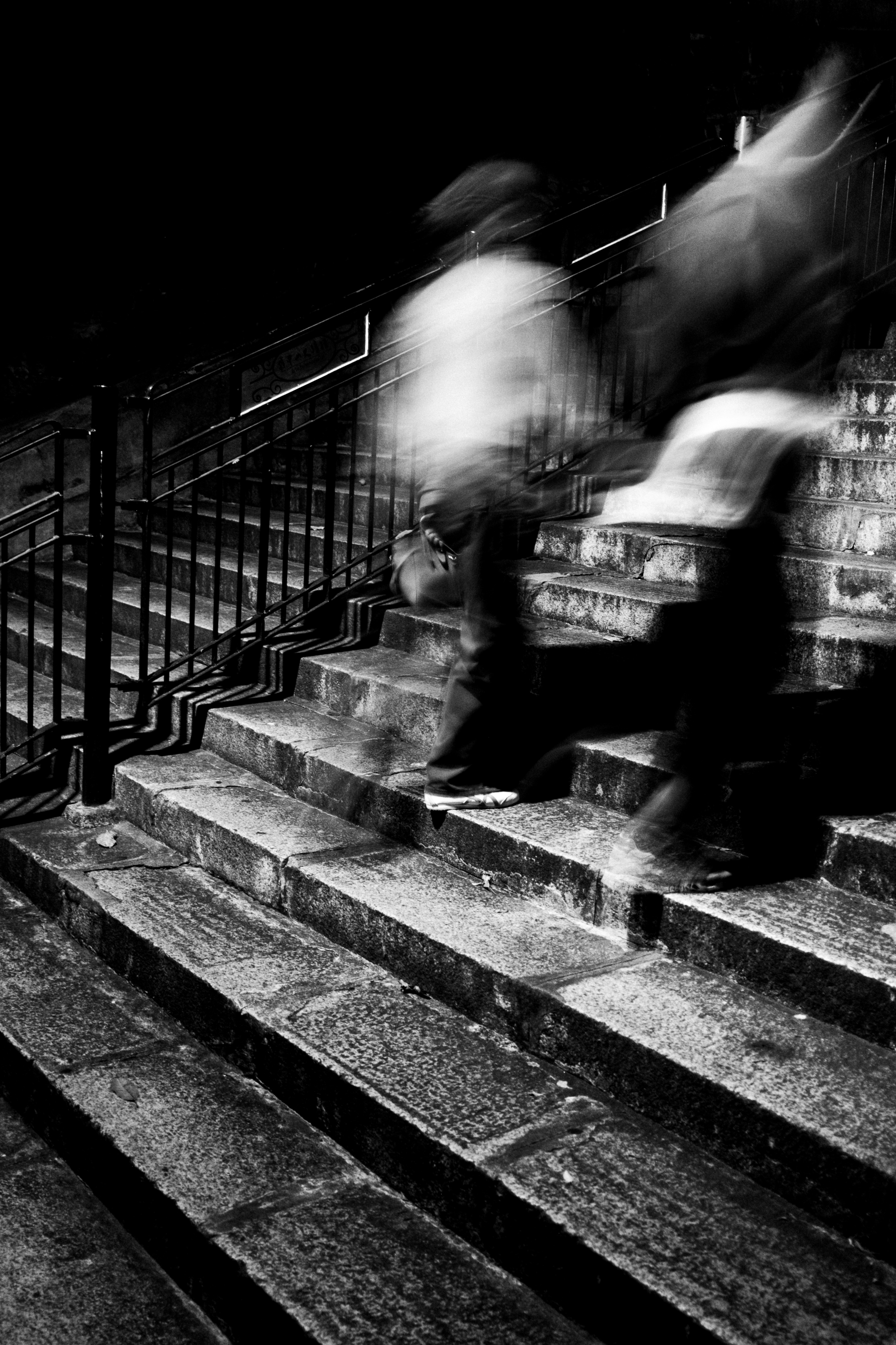 Blurred figures in motion on a stone stairway under contrasting light and shadow.
