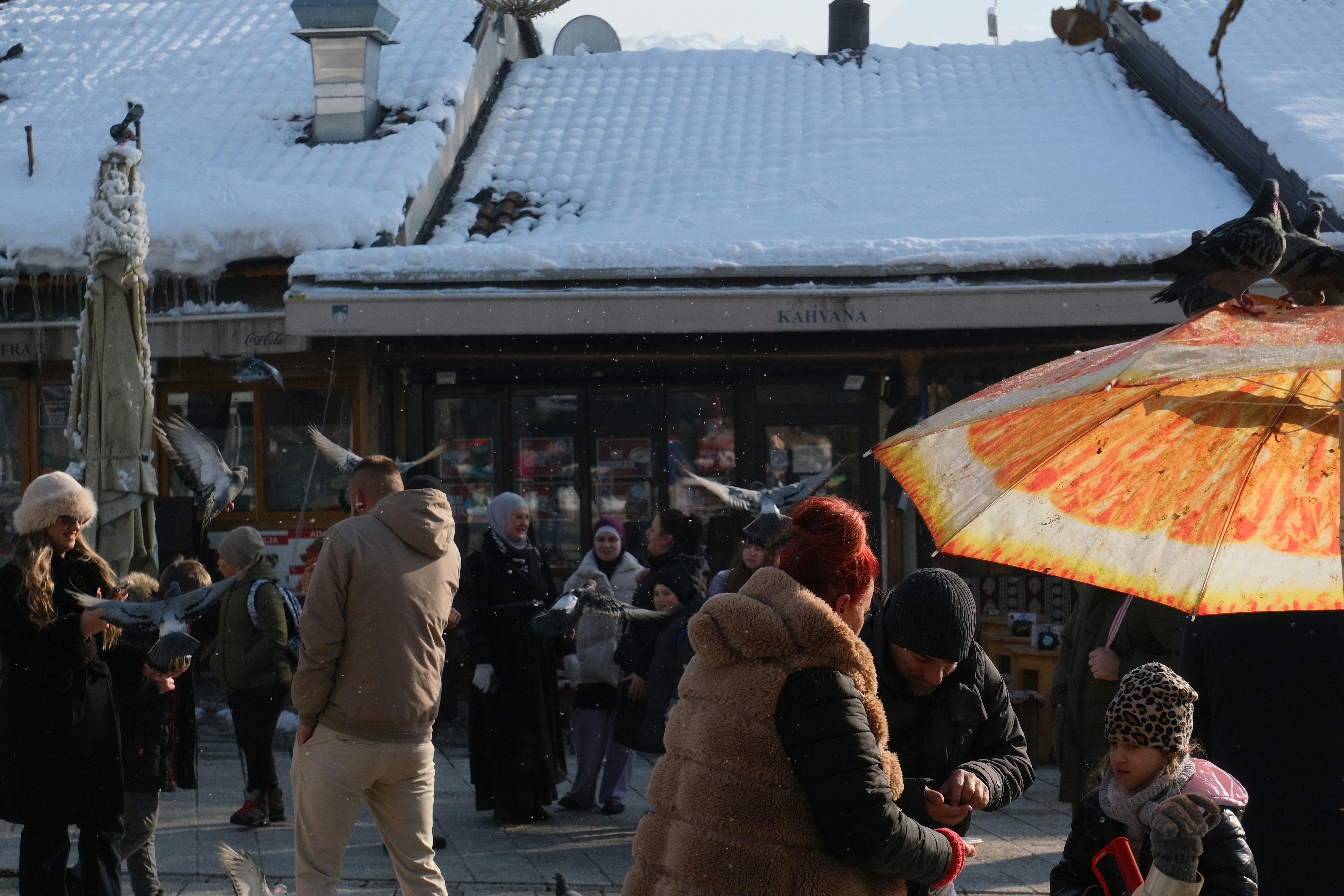Winter Market Toast: People mingle under a sunlit umbrella near a snow‑capped building