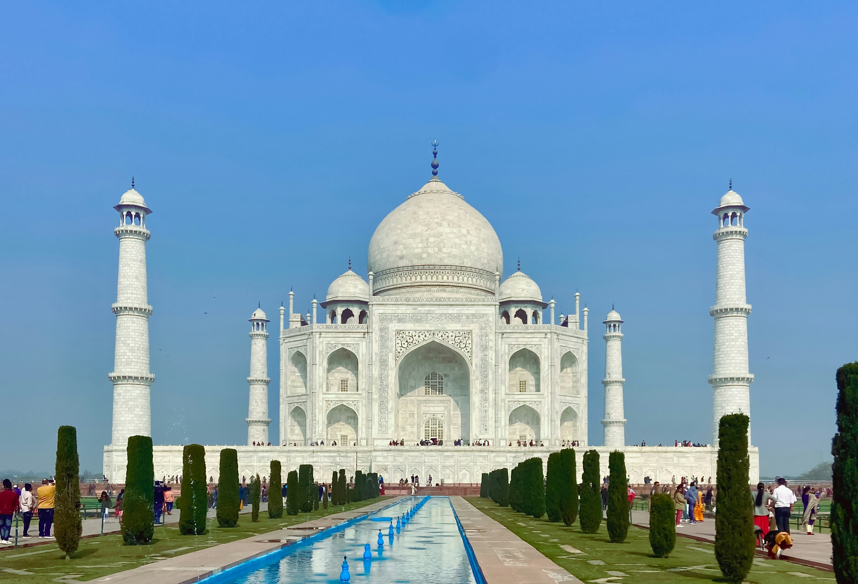 The Taj Mahal framed by a clear blue sky, reflecting in the tranquil waters of the garden's central pool.
