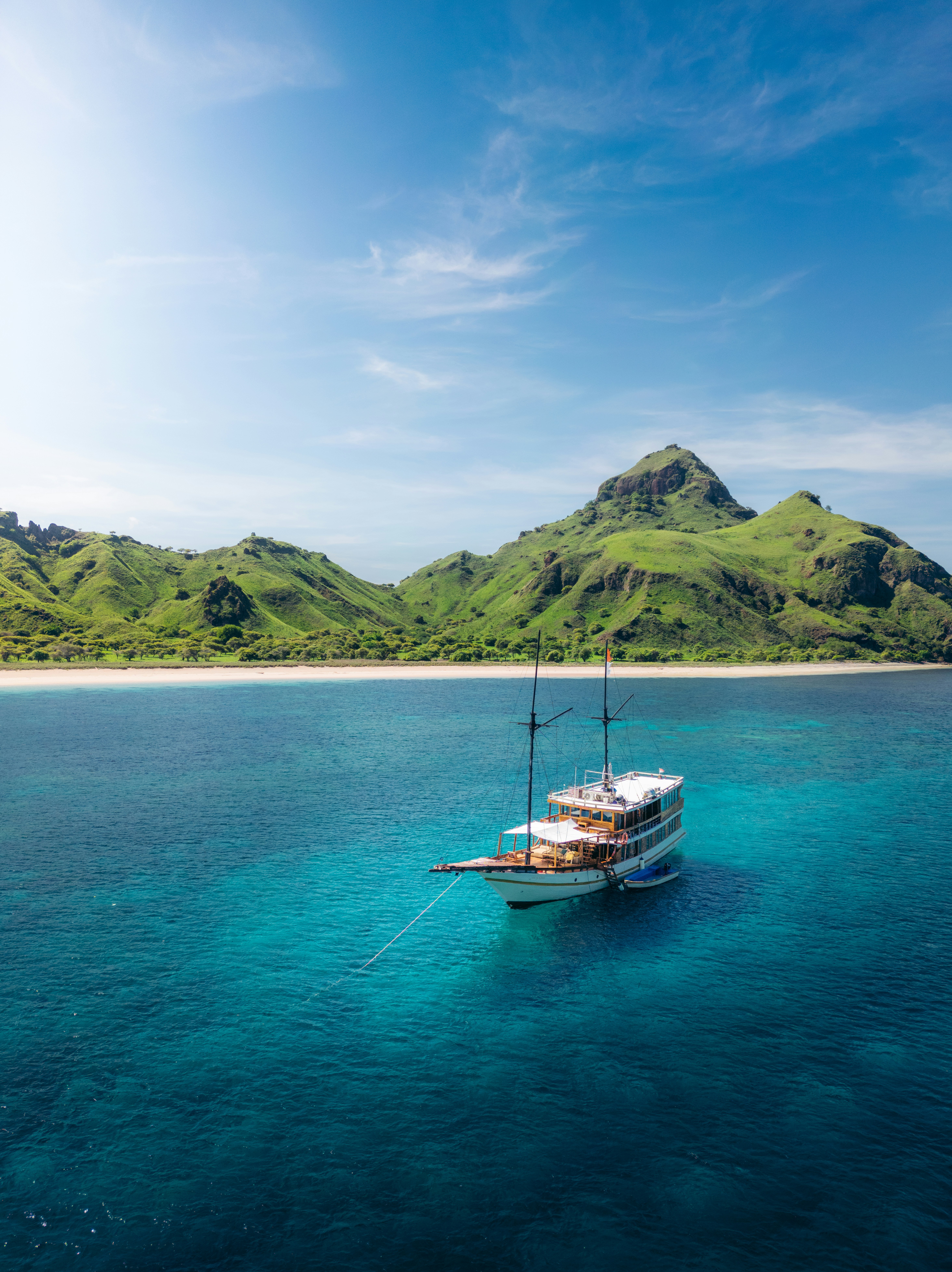 A solitary boat rests in clear turquoise waters, bordered by lush green hills under a bright blue sky.