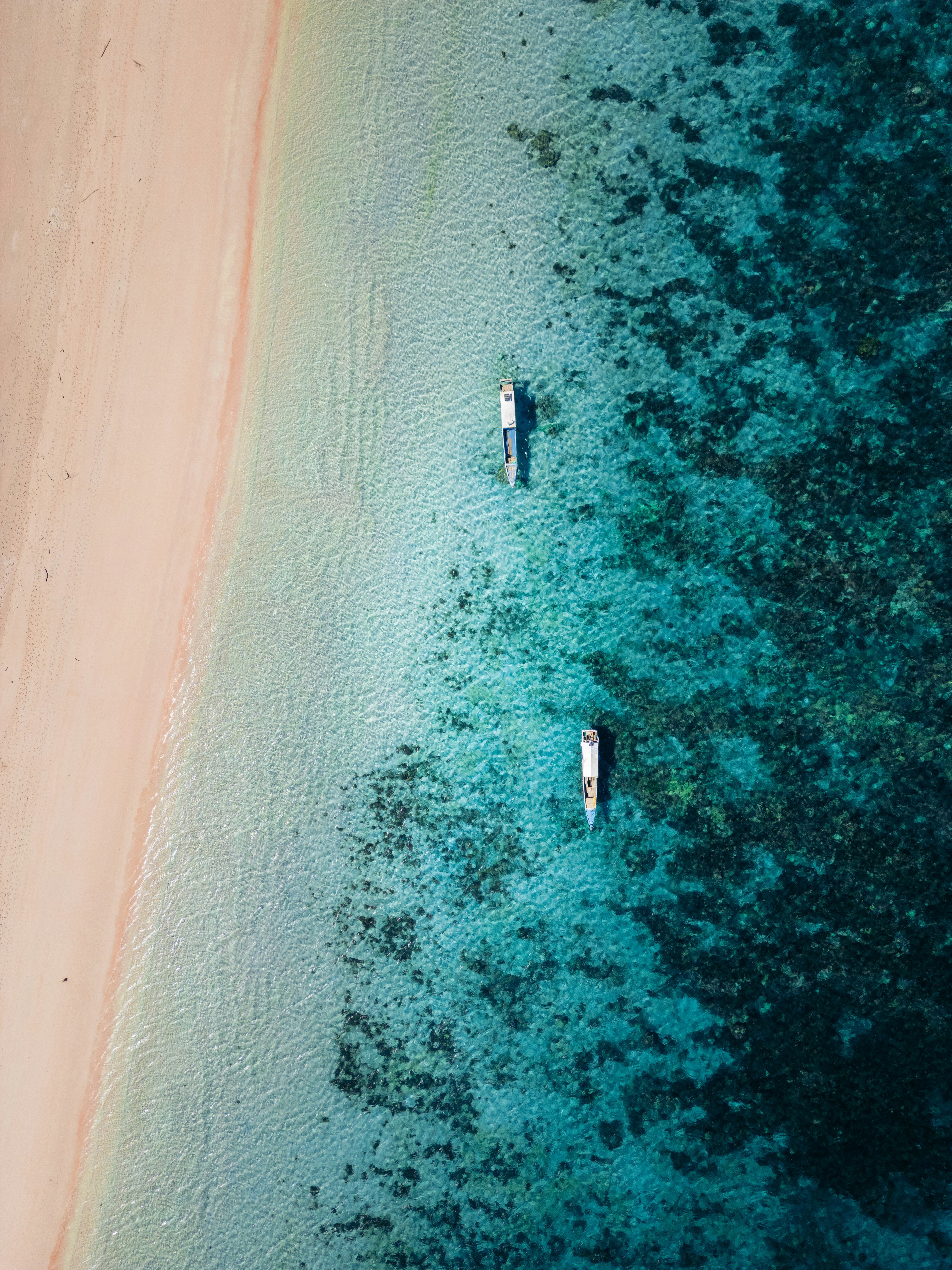 Two boats gliding over crystal-clear turquoise waters near a sandy beach.