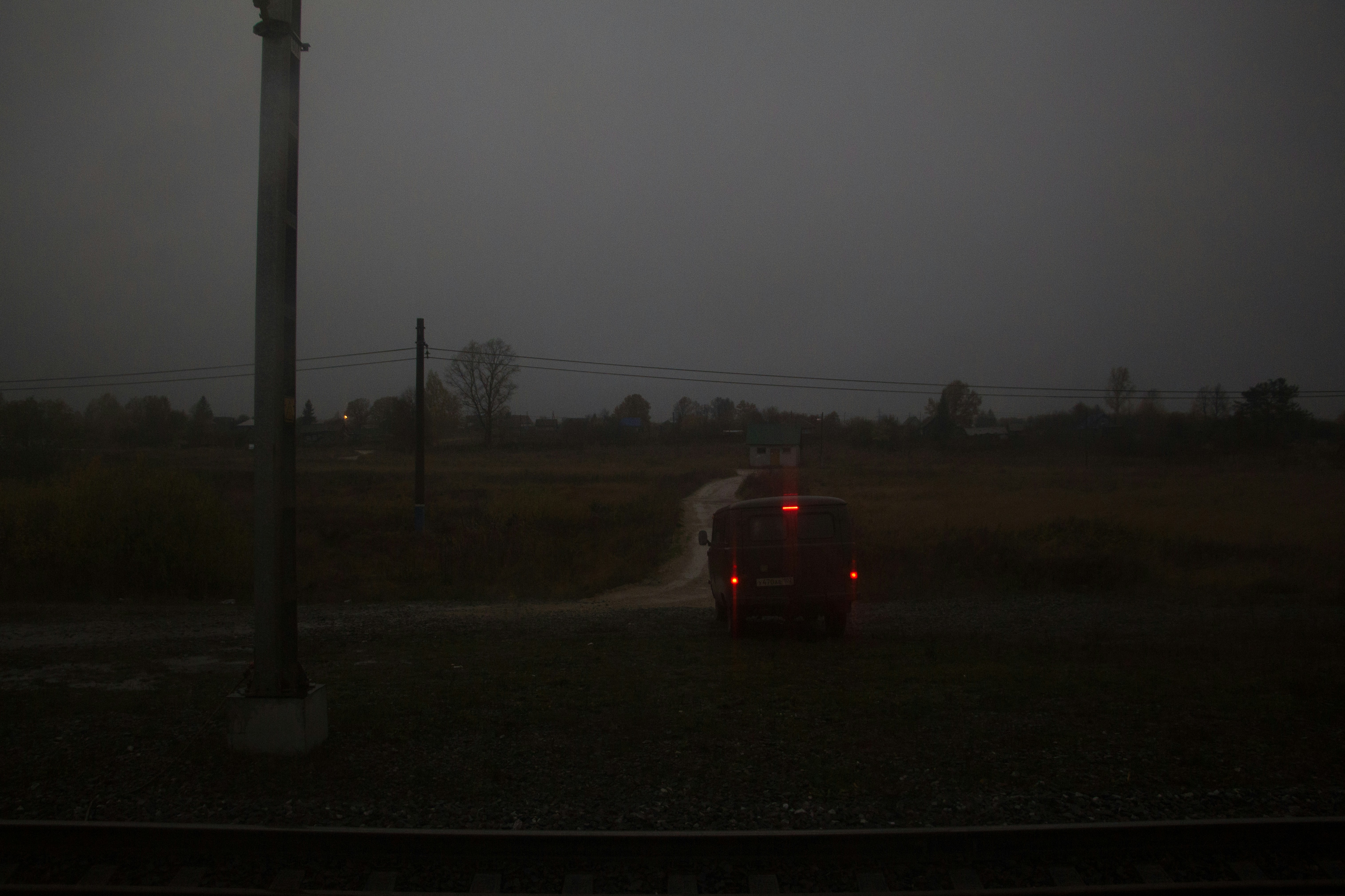 Red Taillights at Dusk: A Lonesome Van Along a Rail-Front Rural Road