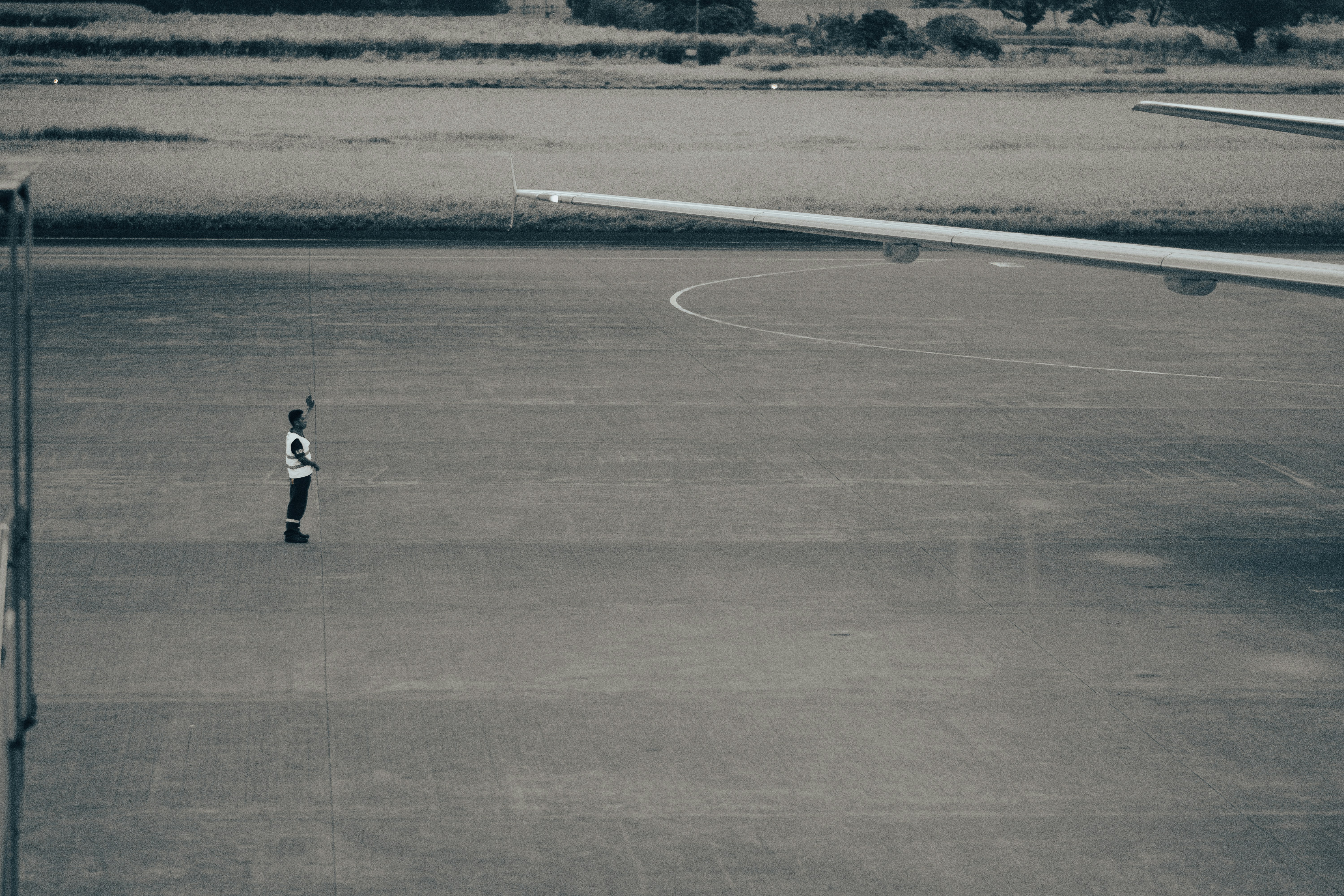 Ground crew member signals on an airport runway, with airplane wing overhead and expansive tarmac visible.