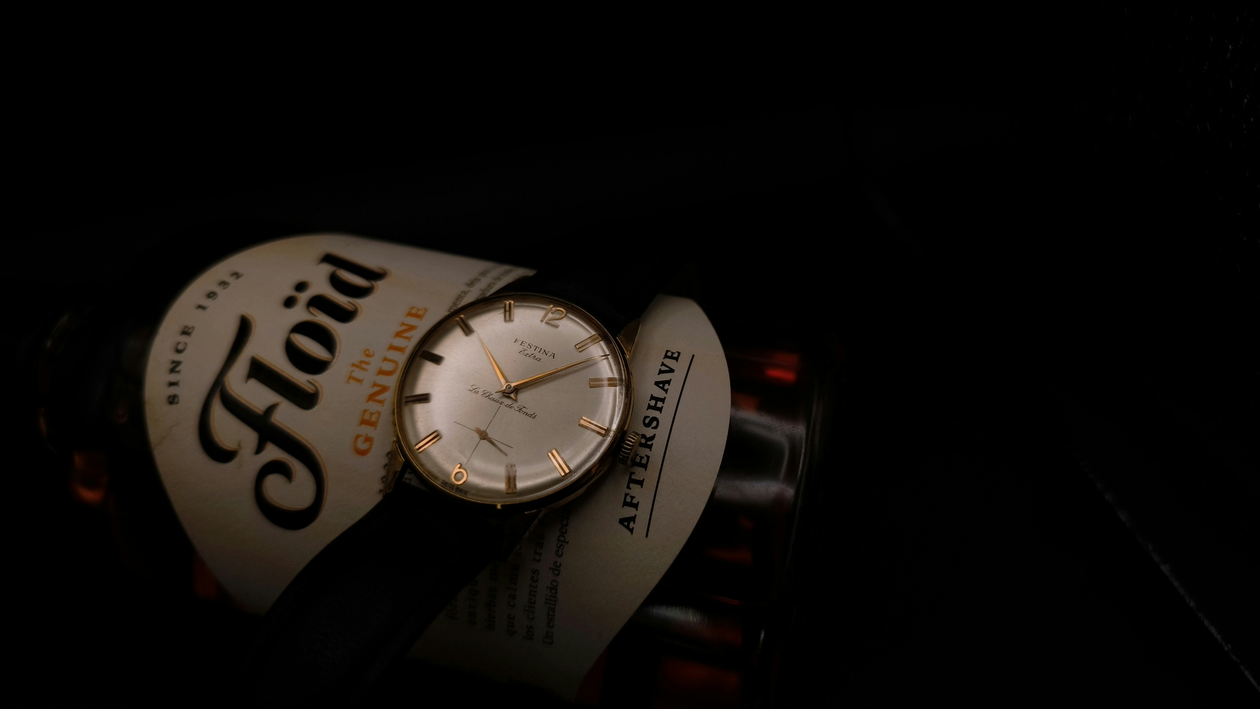 Moonlit Dial: A Silver Watch Anchoring a Floid Aftershave Label in Deep Shadow