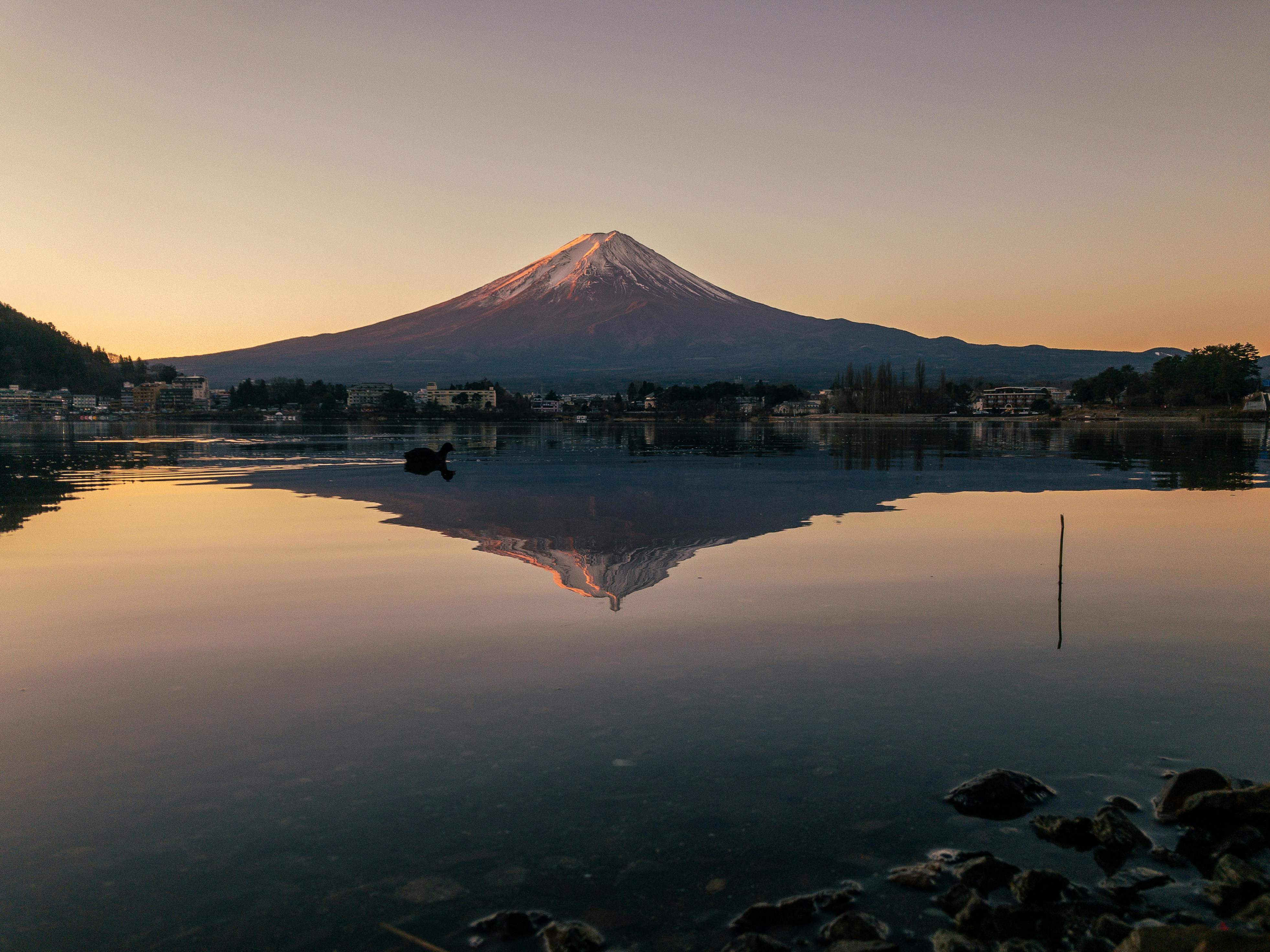 Snow-capped mountain reflected in calm waters at sunrise with a pastel sky.