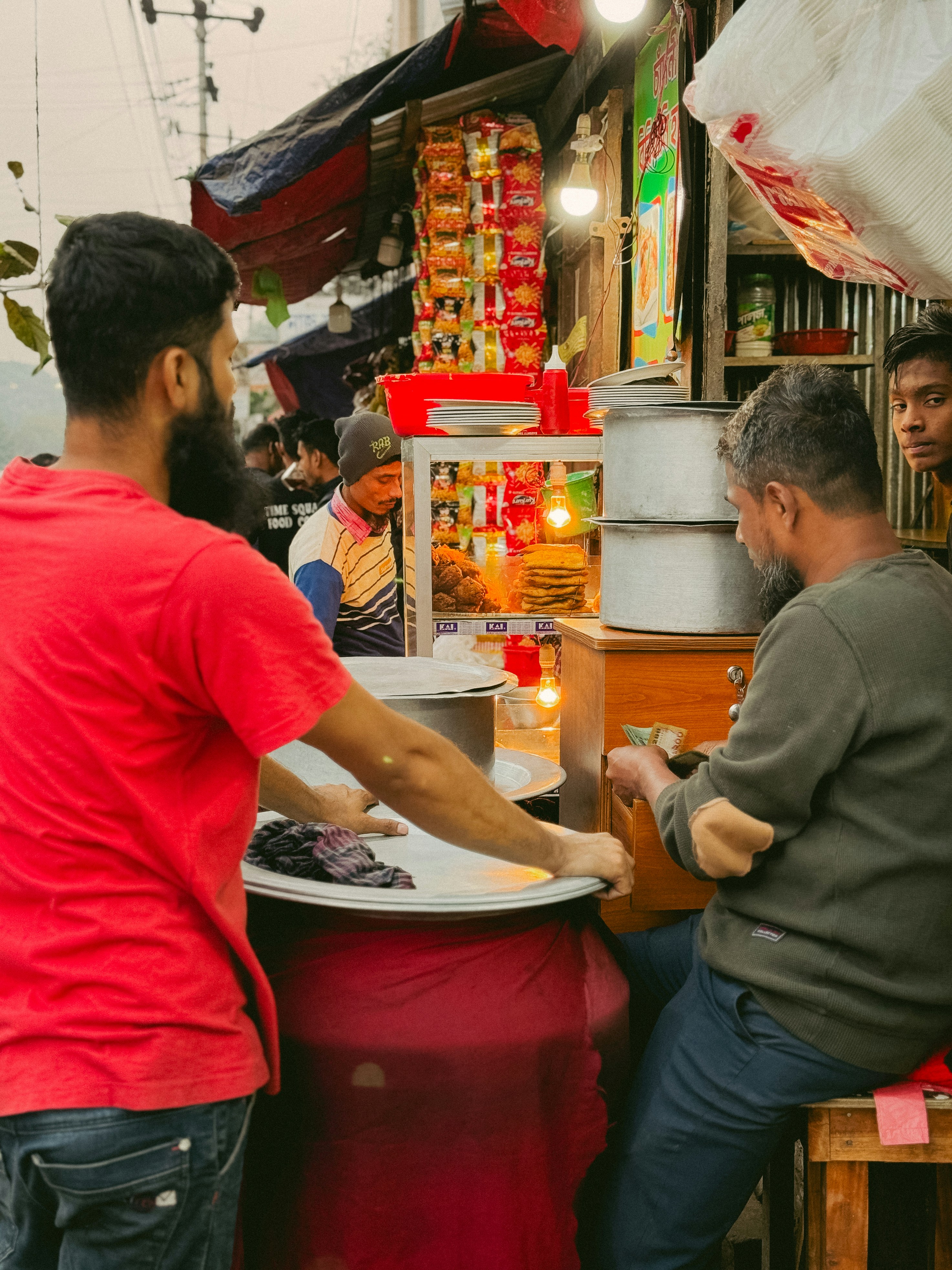 Red-Shirt Vendor Orchestrates a Bustling Street Food Stall Under Market Lights