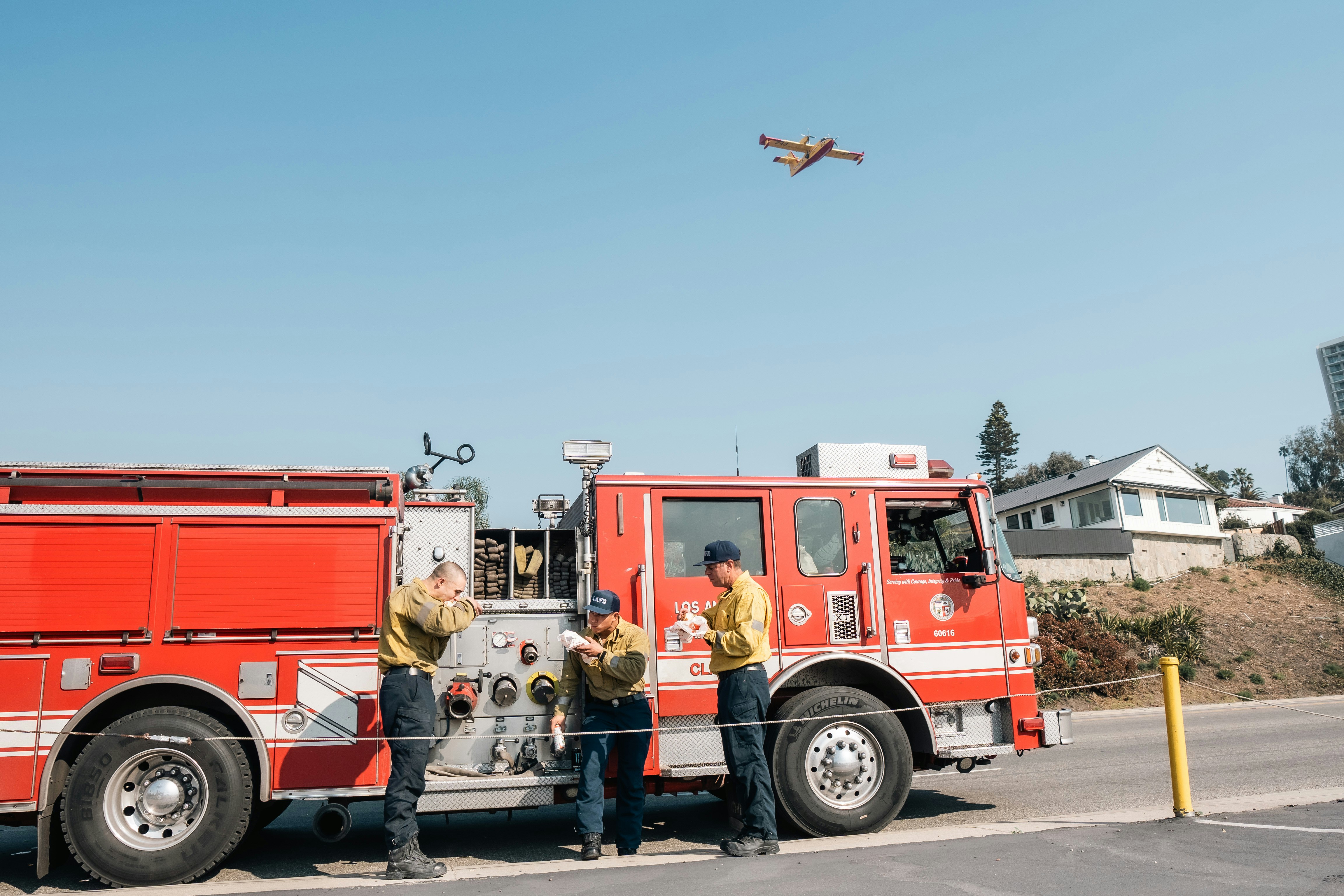 Red Engine, Skyward Watch: Firefighters Stand Guard as an Airplane Passes Overhead