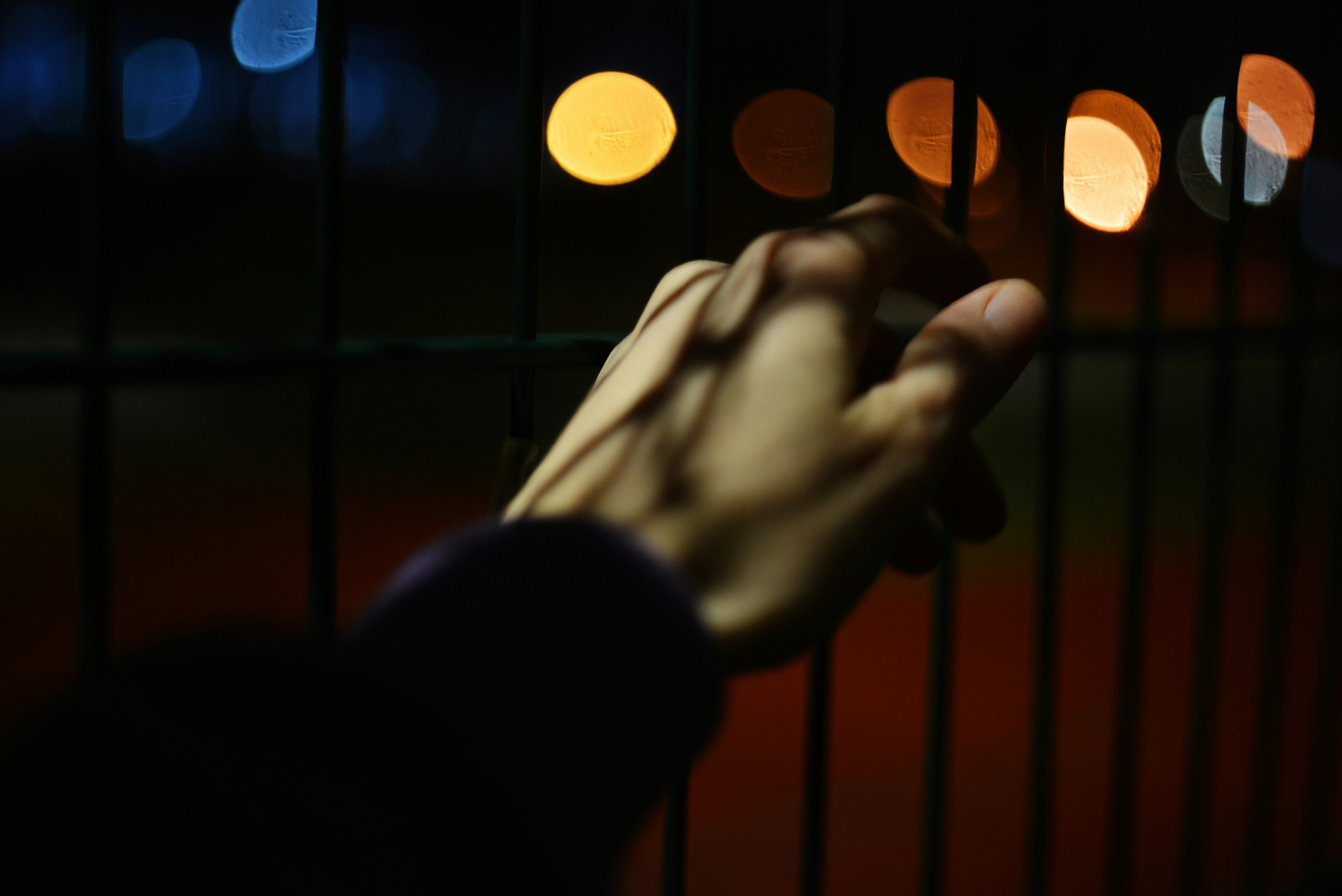 Grip in the Dark: Fingers Against Iron Bars with Neon Bokeh
