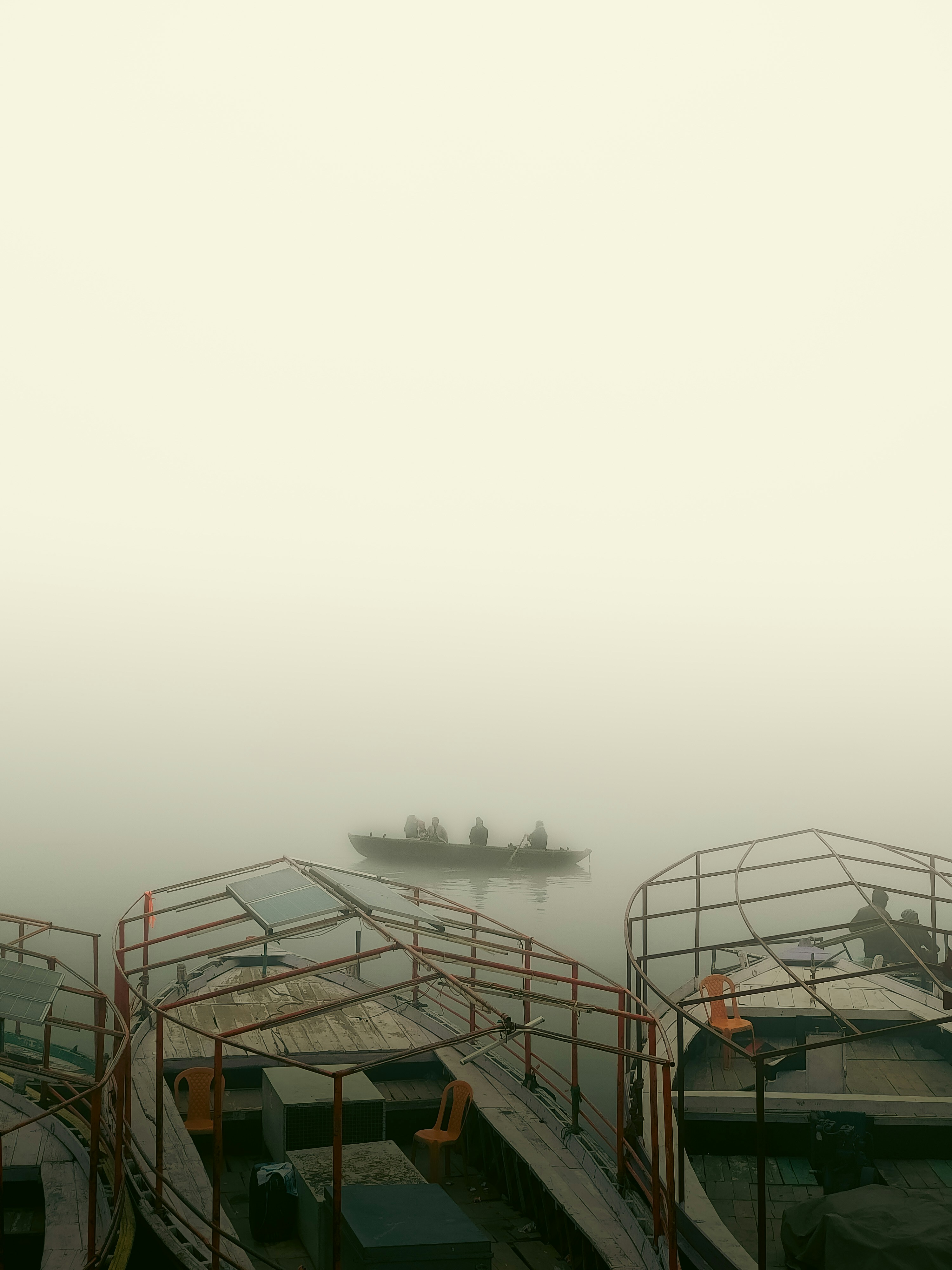 Misty river scene with several boats anchored at the foreground and a distant boat shrouded in fog. The atmosphere evokes a sense of calm and isolation.