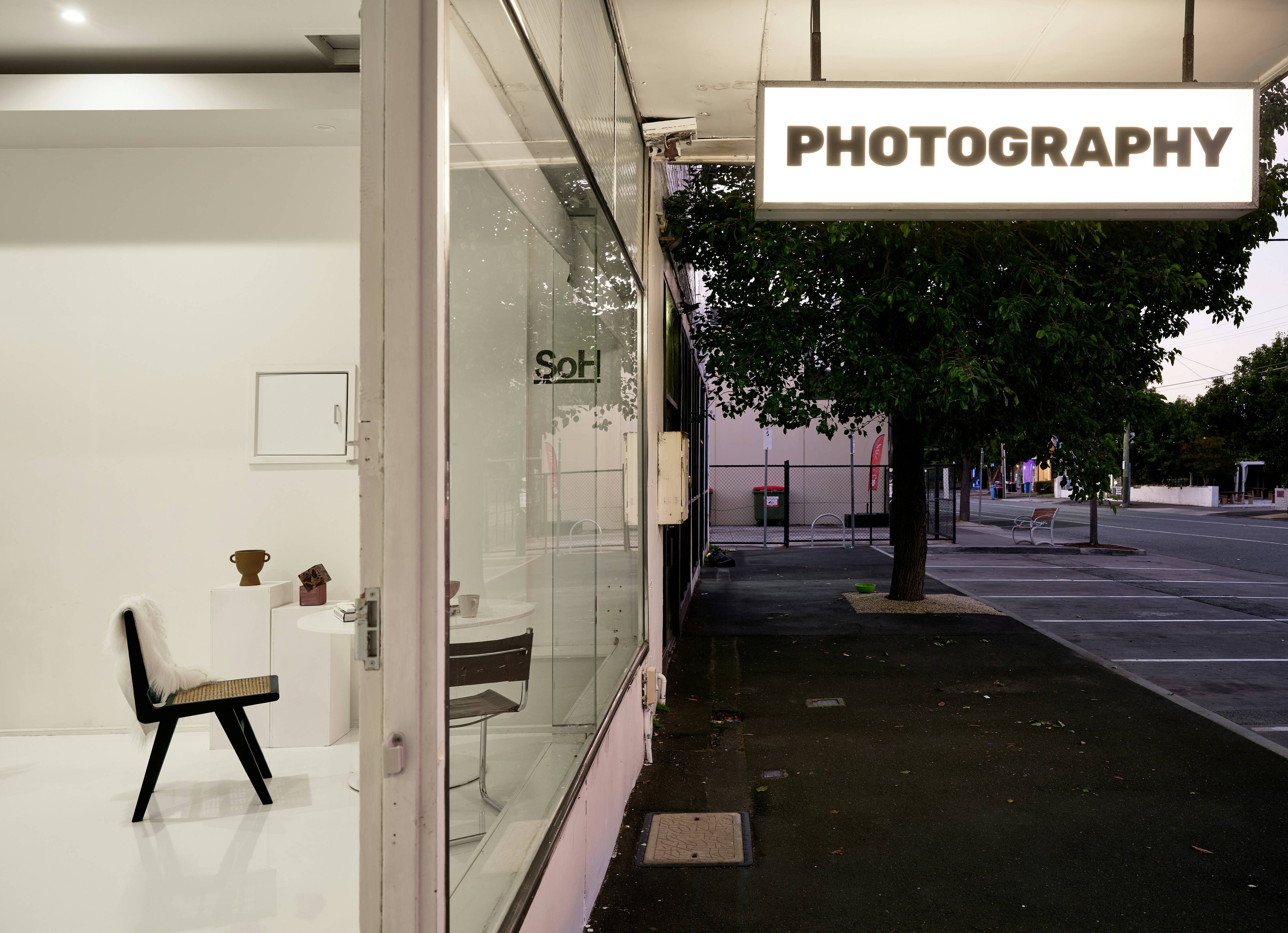 Minimalist studio interior with warm lighting contrasts the twilight street scene under a glowing photography sign.