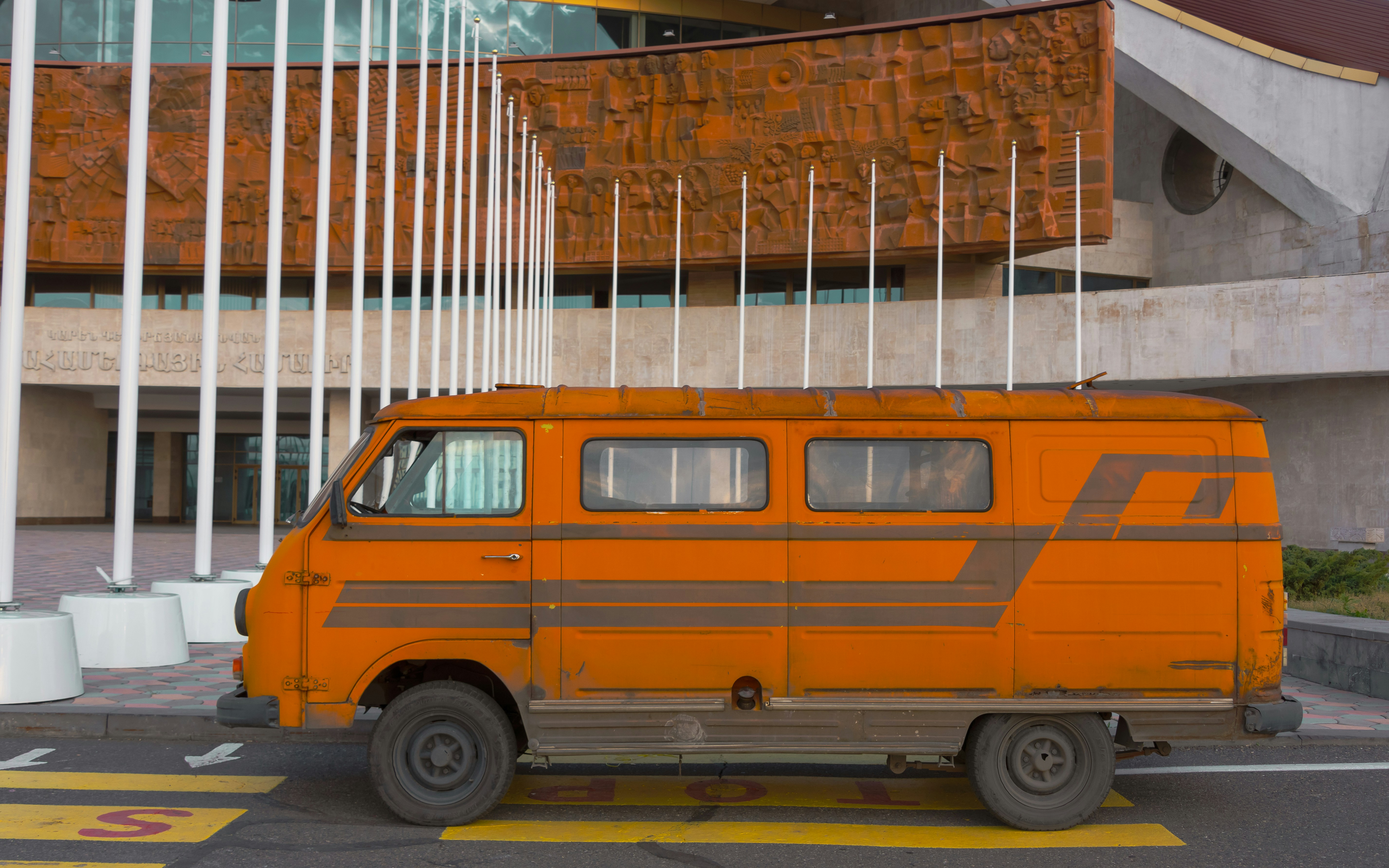 Orange RAF-2203 minibus parked in front of a contemporary building with vertical white poles.