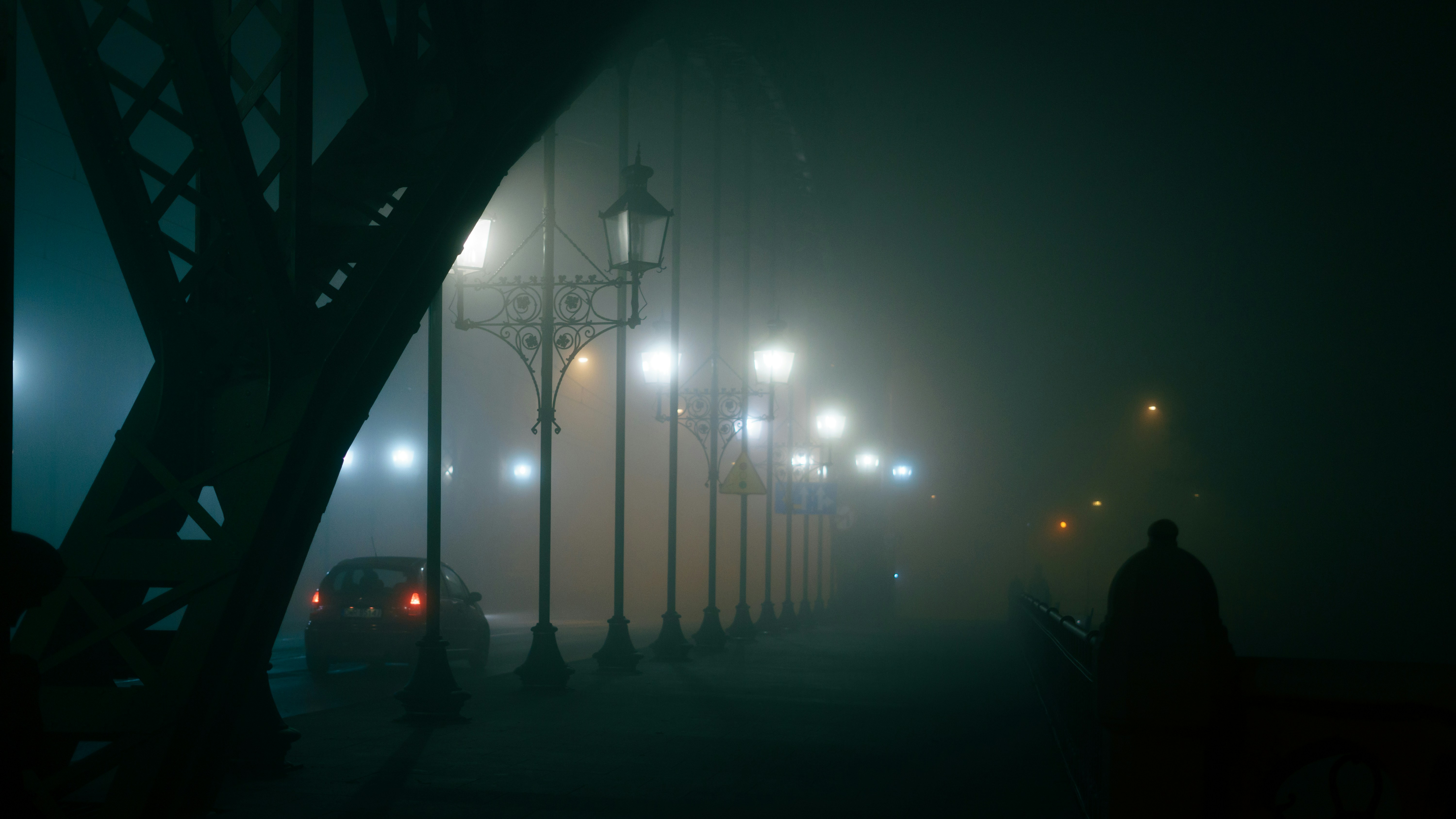 Foggy street with glowing lanterns and silhouetted figures under an ornate bridge.
