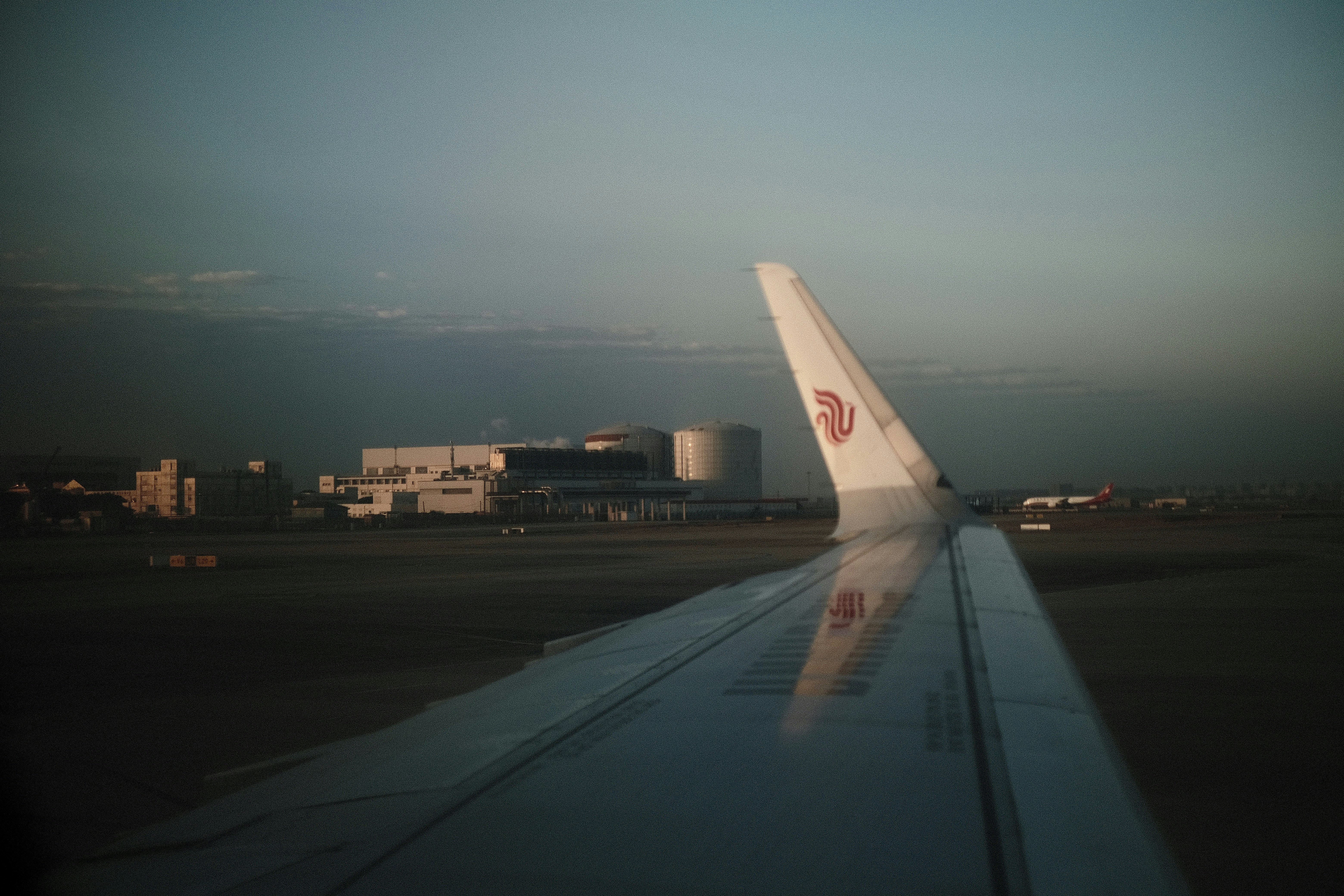 Airplane wing reflecting the soft light of dusk, with airport buildings in the background.