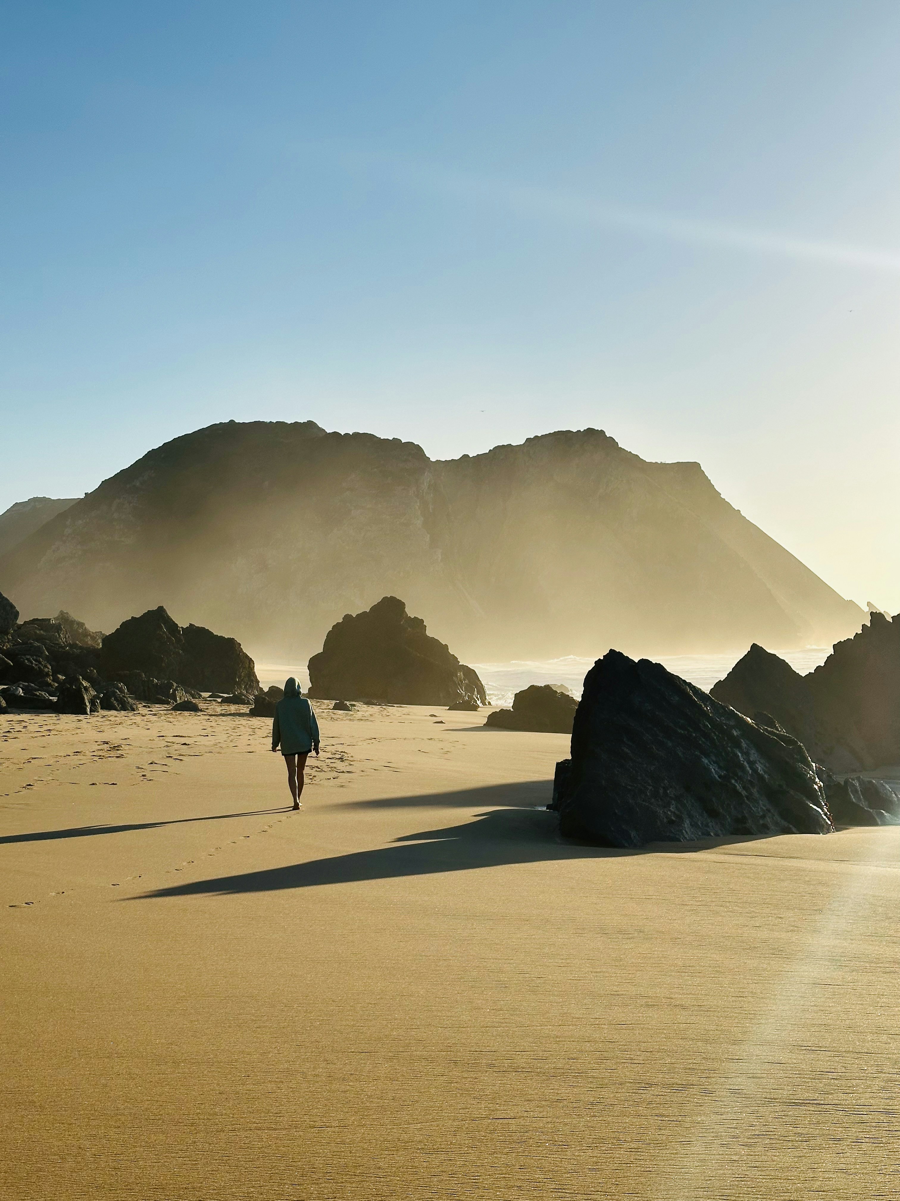 A person walking on a sandy beach next to large rocks photo – Free ...