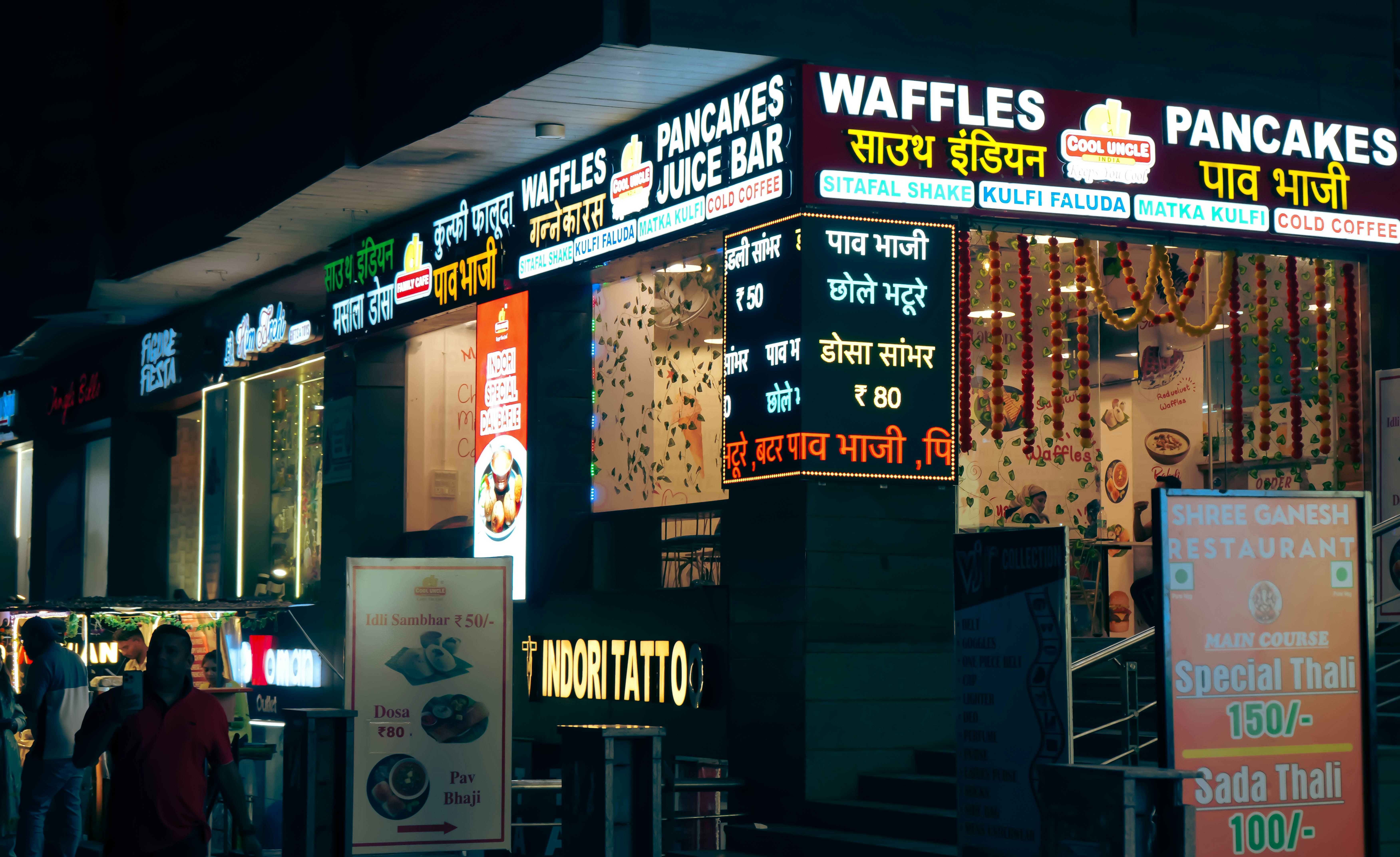 Illuminated storefronts with vibrant signage advertising waffles and pancakes at night.