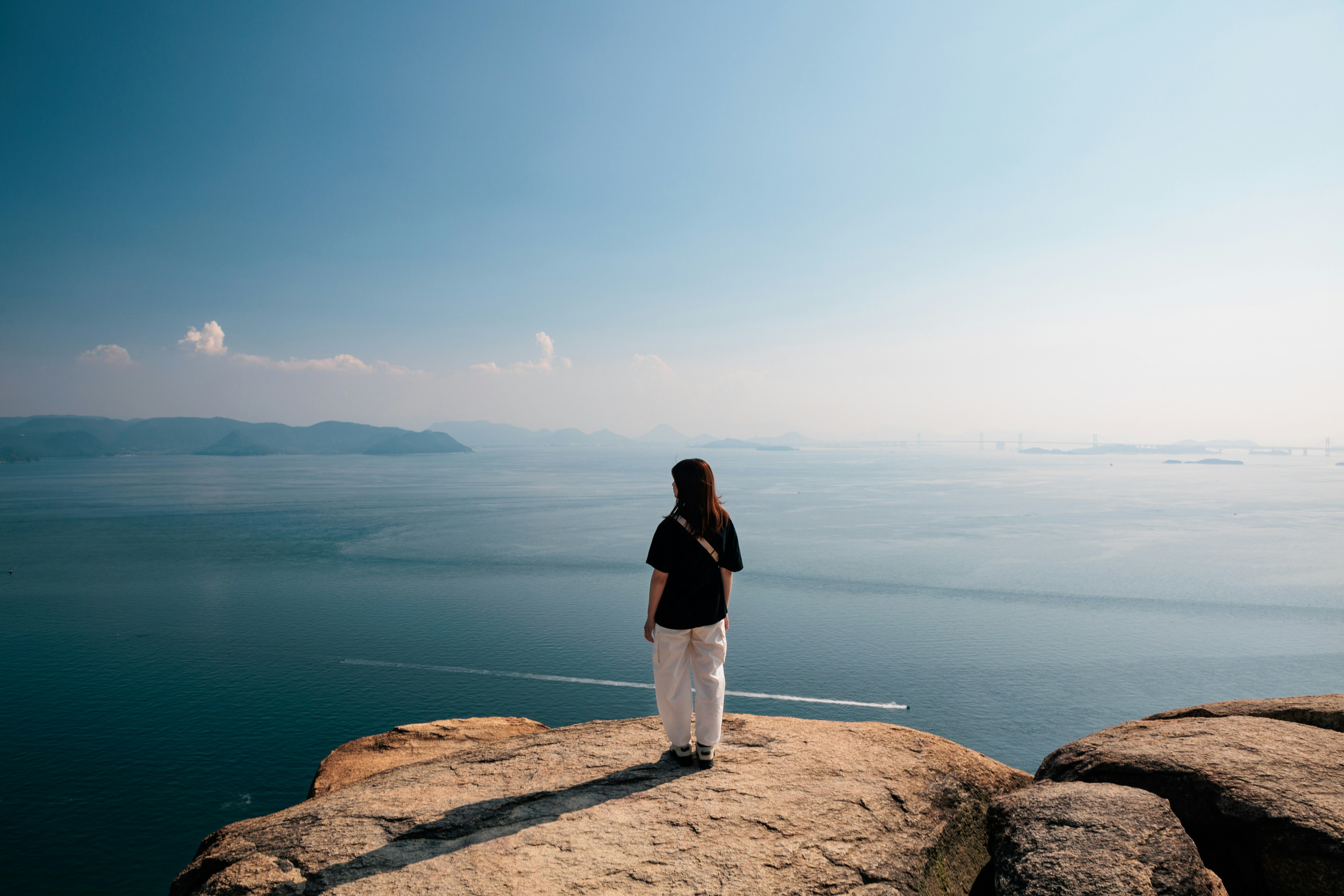Edge of Solitude: A lone figure on a cliff overlooking a vast sea horizon