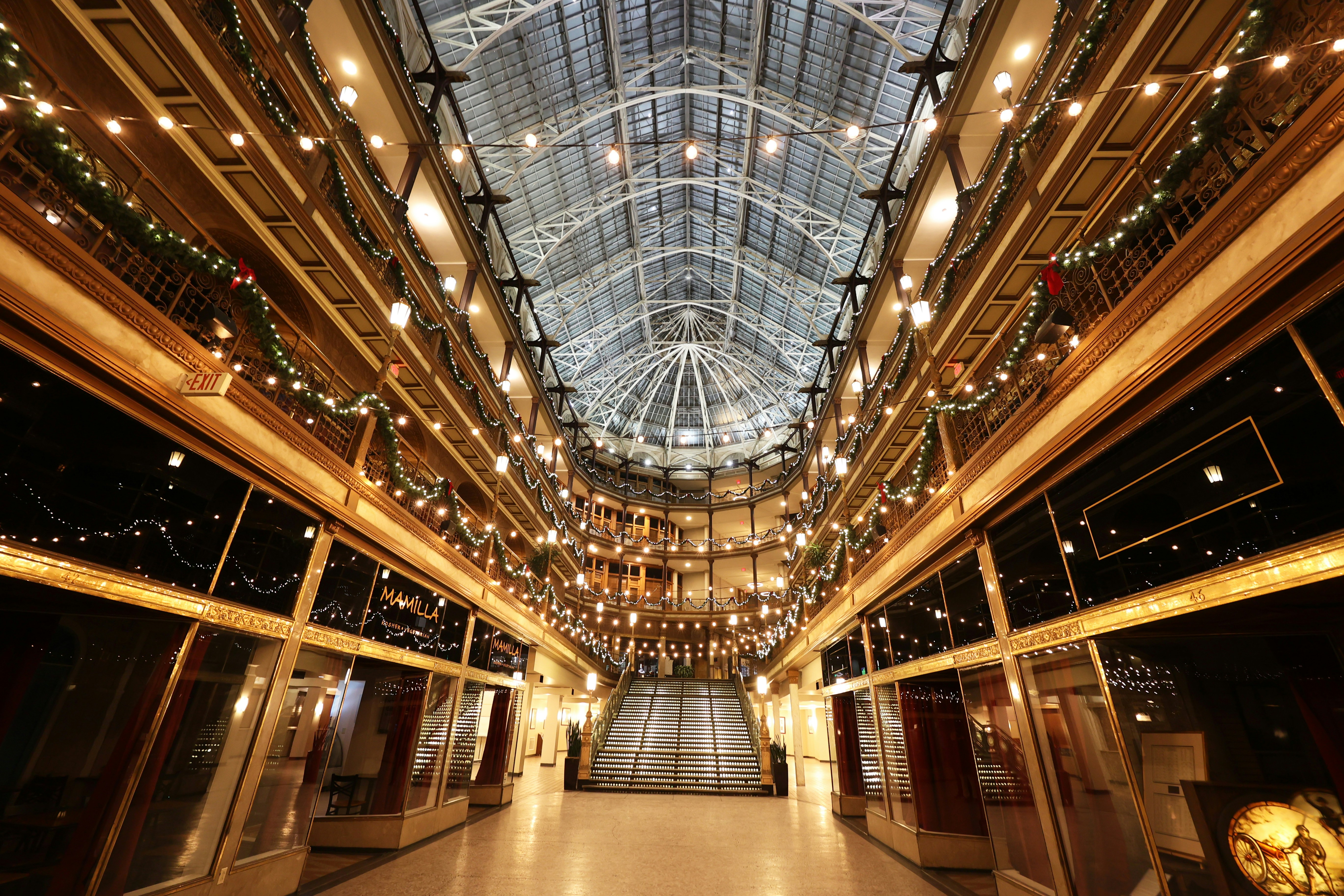 Grand arcade with ornate glass ceiling, adorned with festive string lights.