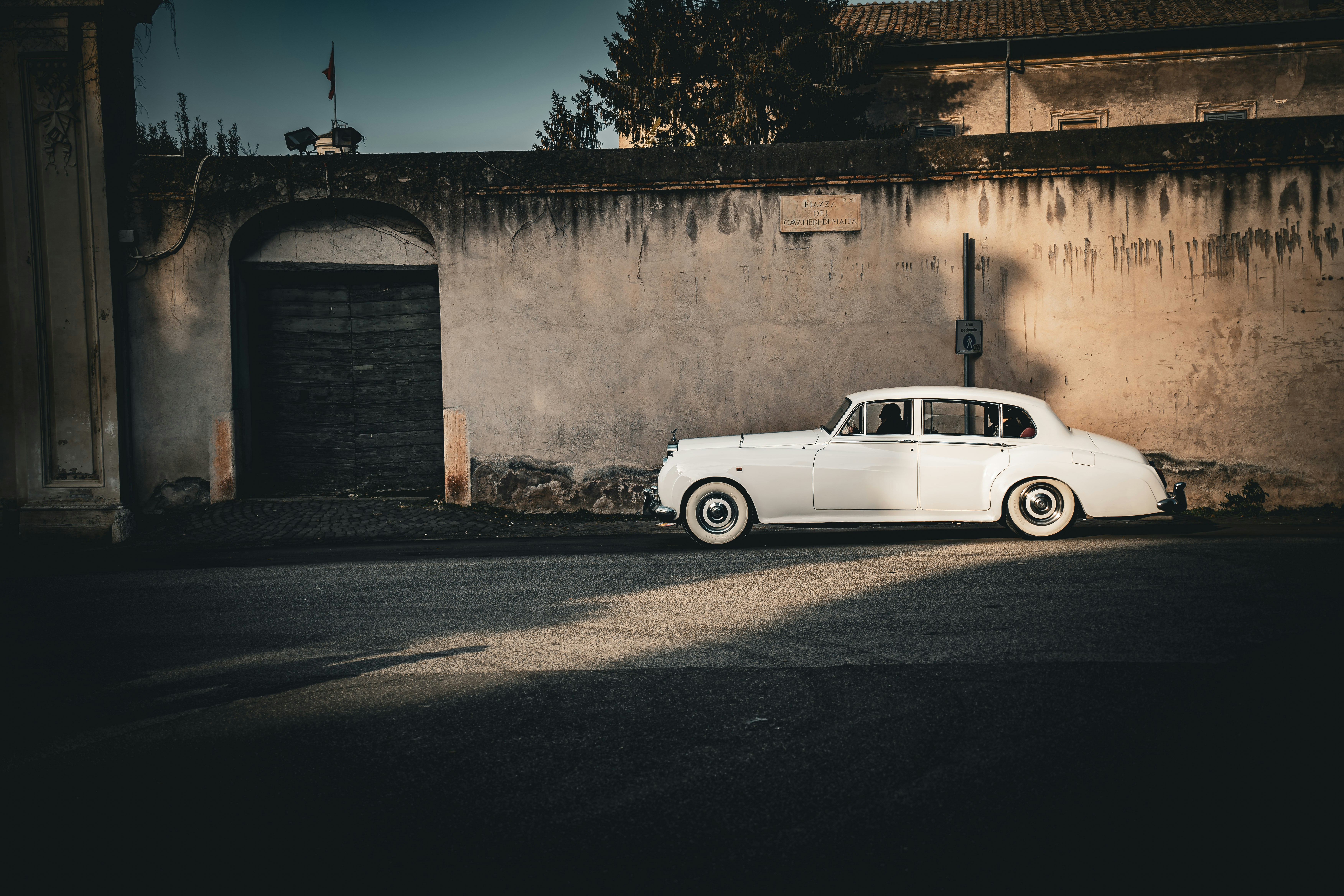 White vintage car parked against an aged stone wall, bathed in warm afternoon light.
