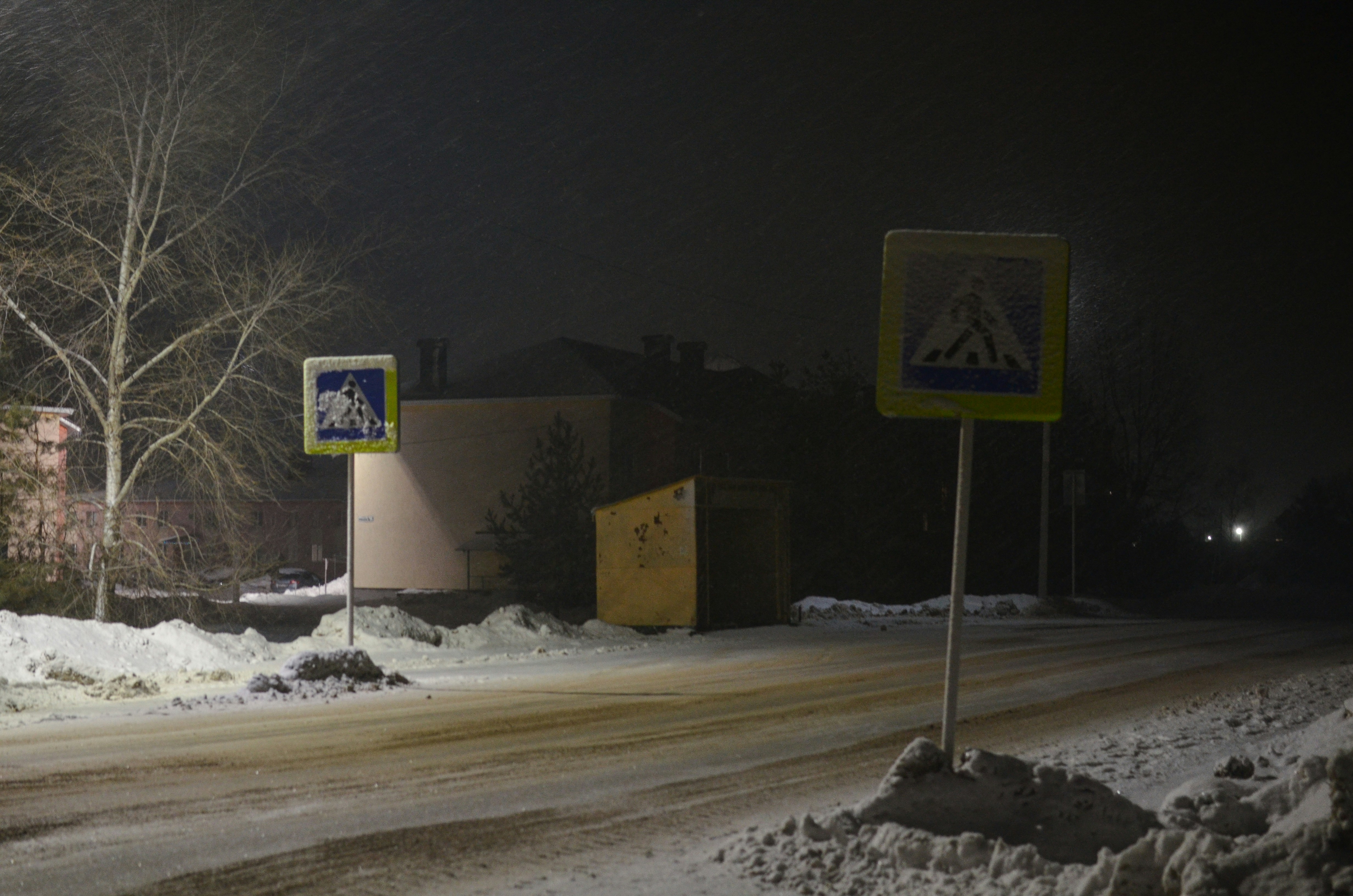 Snow-covered road with illuminated pedestrian signs under a dimly lit sky.