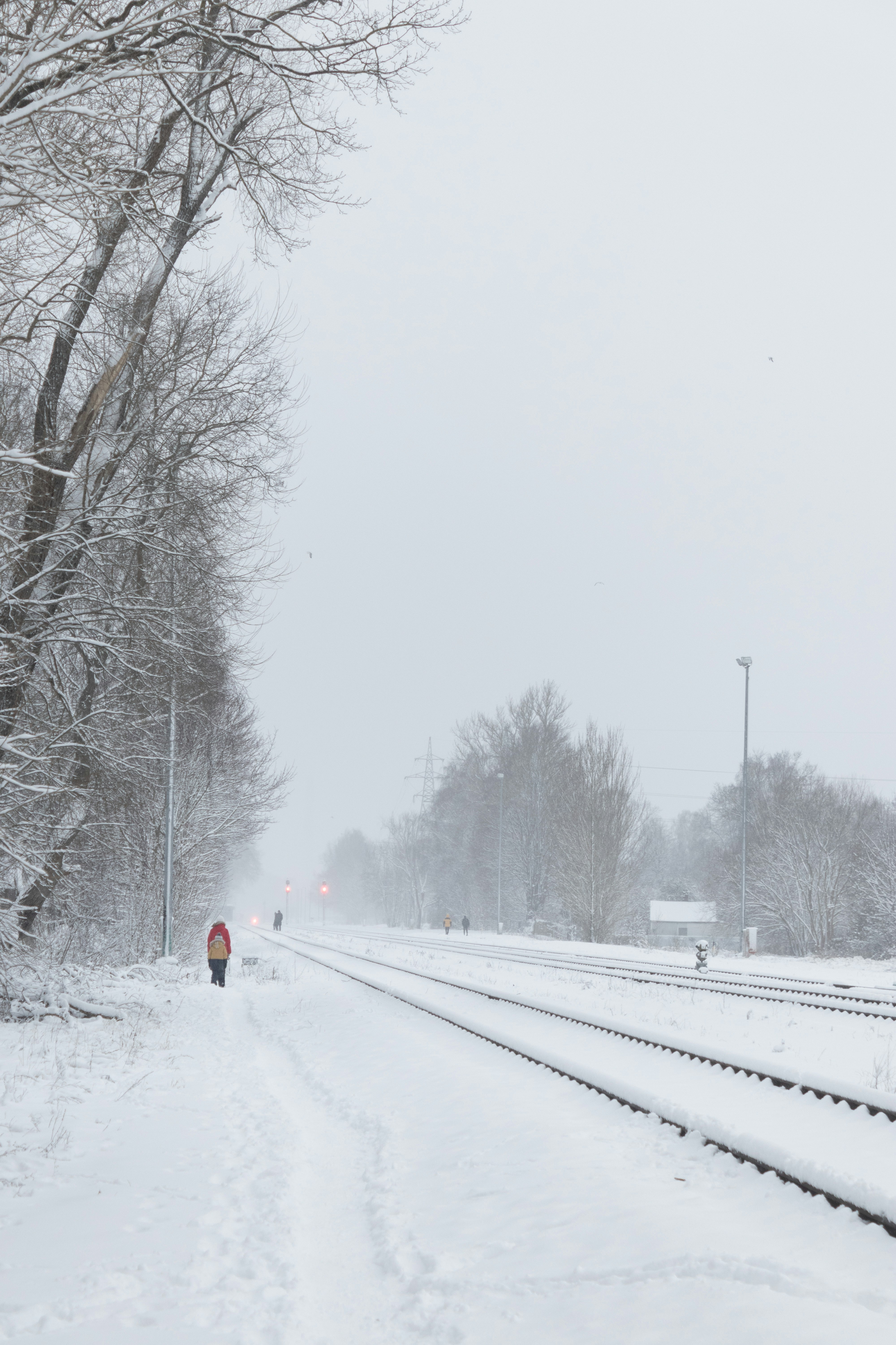 Winter Rails: A Lone Figure in Orange on Snow-Blanketed Tracks