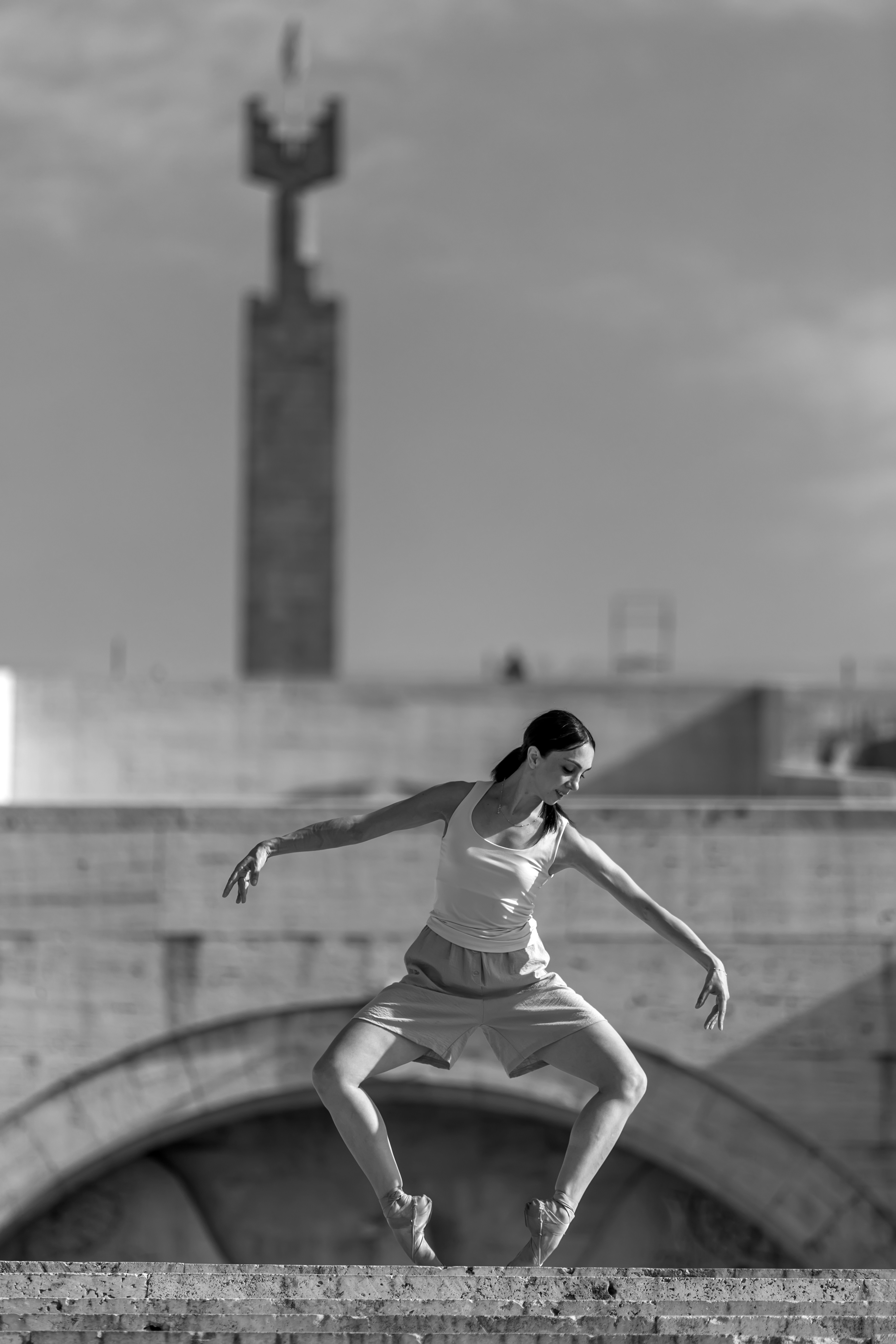 Midair on Stone: A dancer poised above the arch beneath a distant monument