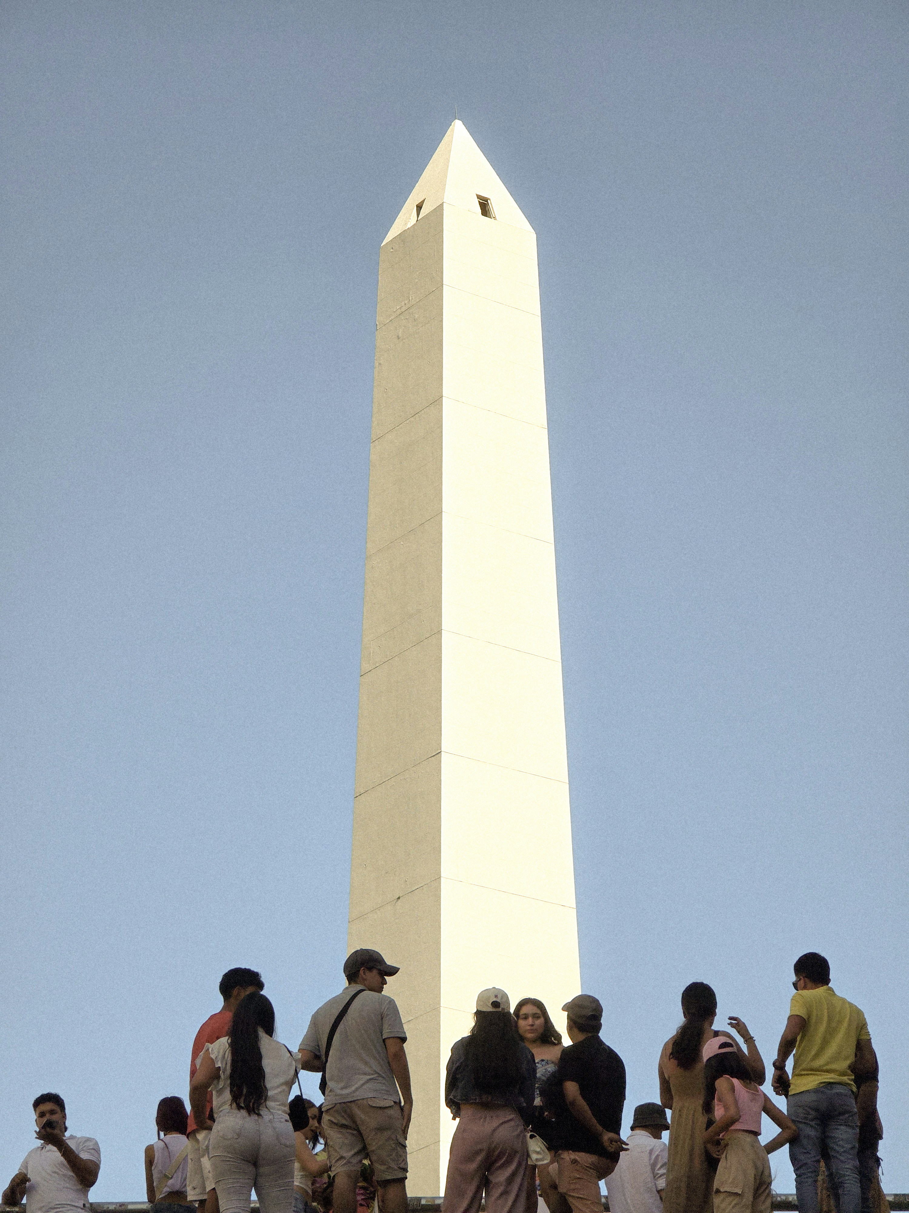 Cerulean Spire Over a Crowded Plaza: A White Obelisk at Noon