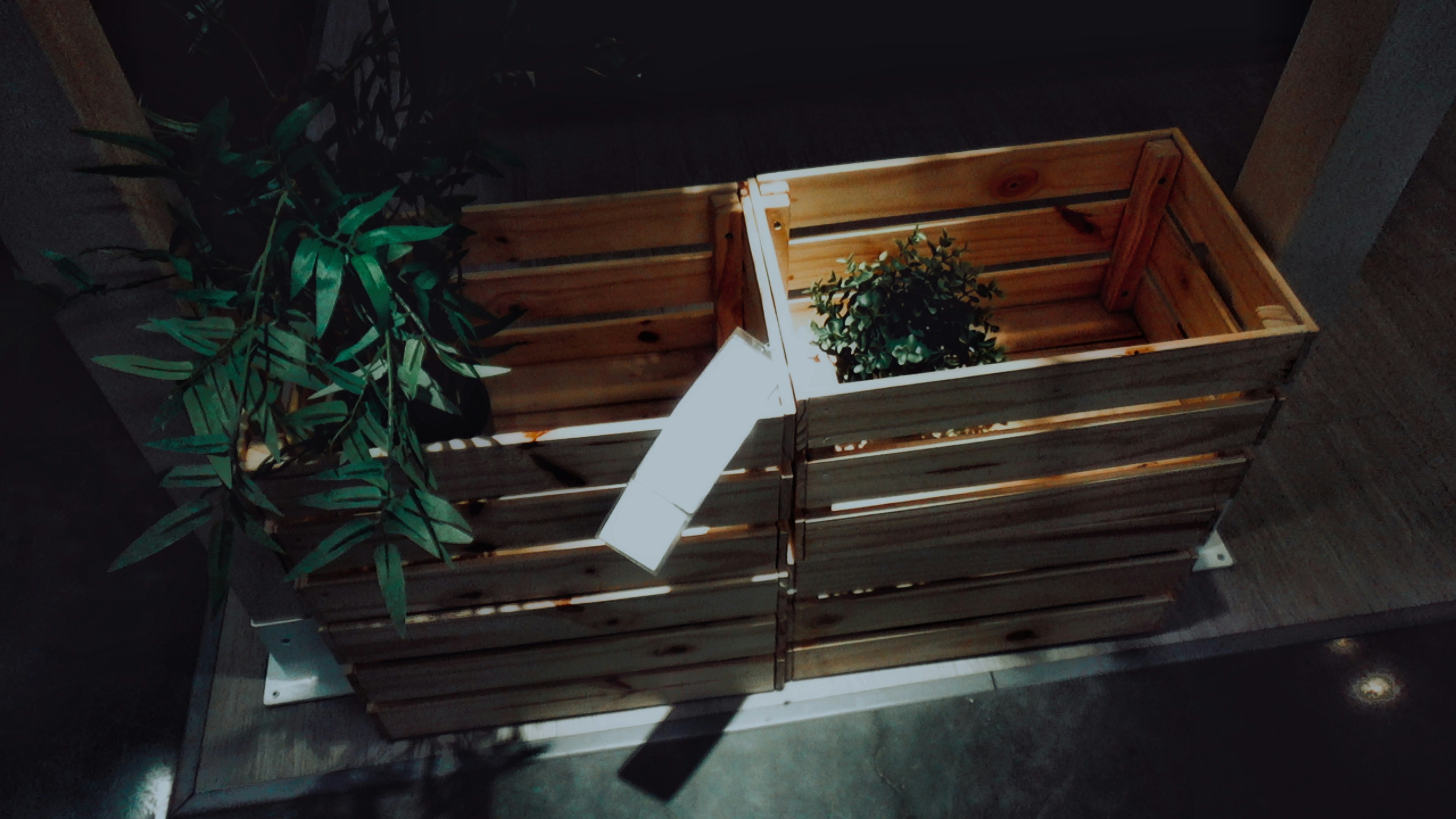 A White Beam Bridges Two Wooden Planters in a Dim Indoor Nook