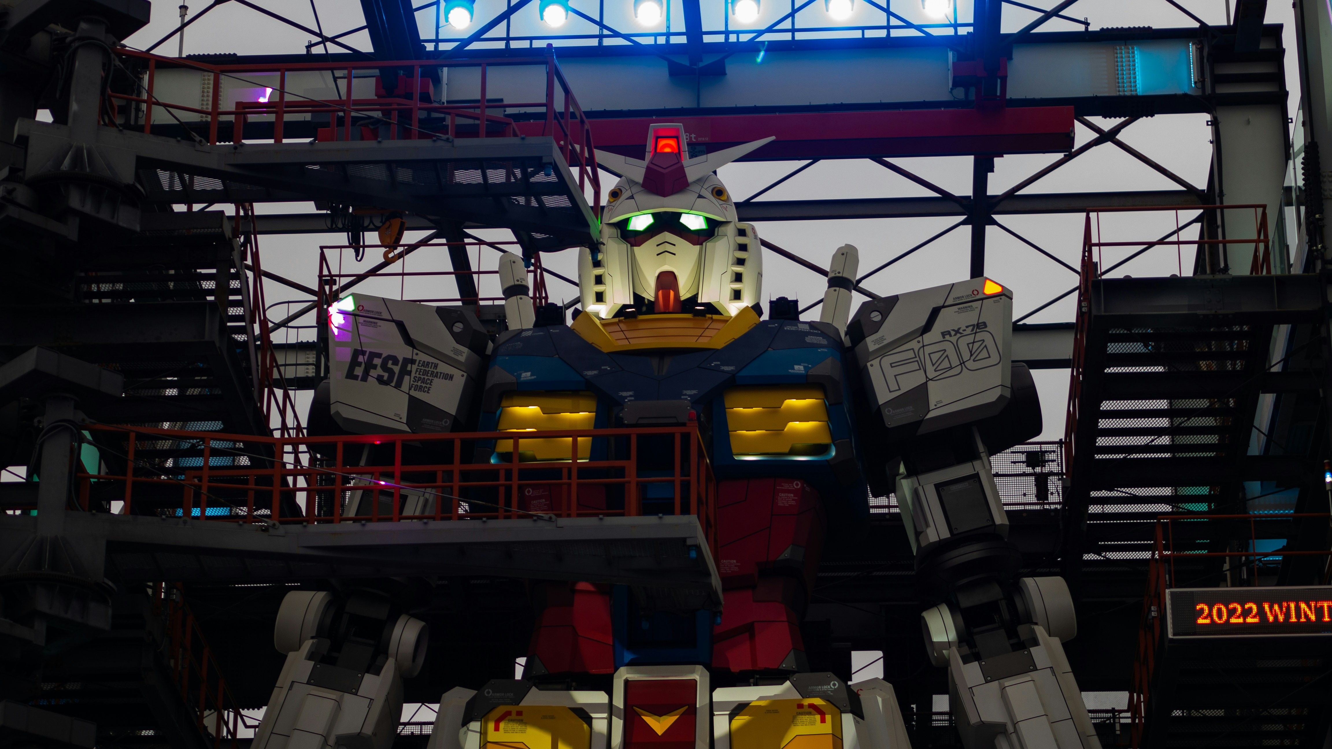 Neon Titan: Gundam Emerges Through the Workshop Scaffolding