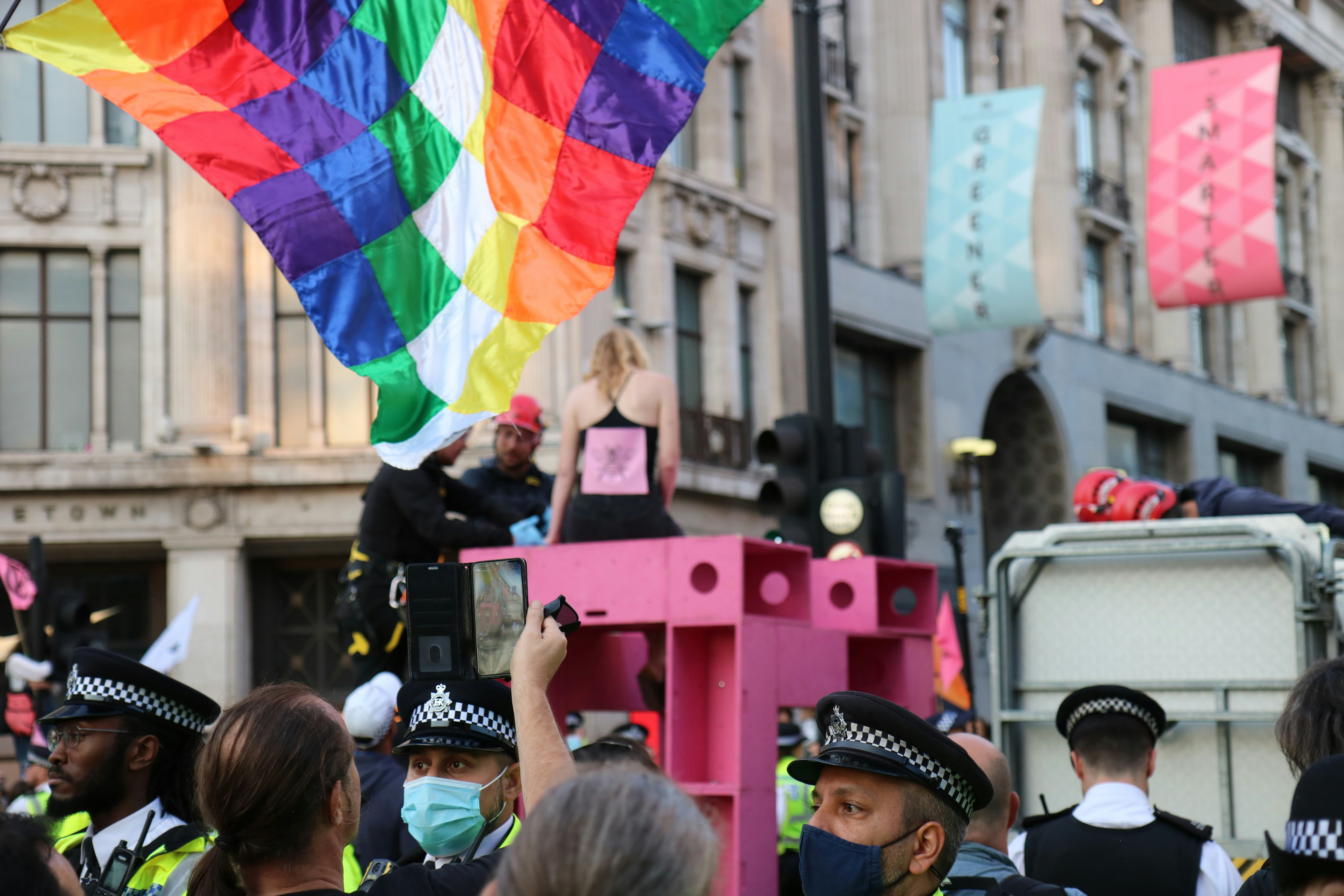 Colorful protest scene with vibrant flags and police presence on a city street.