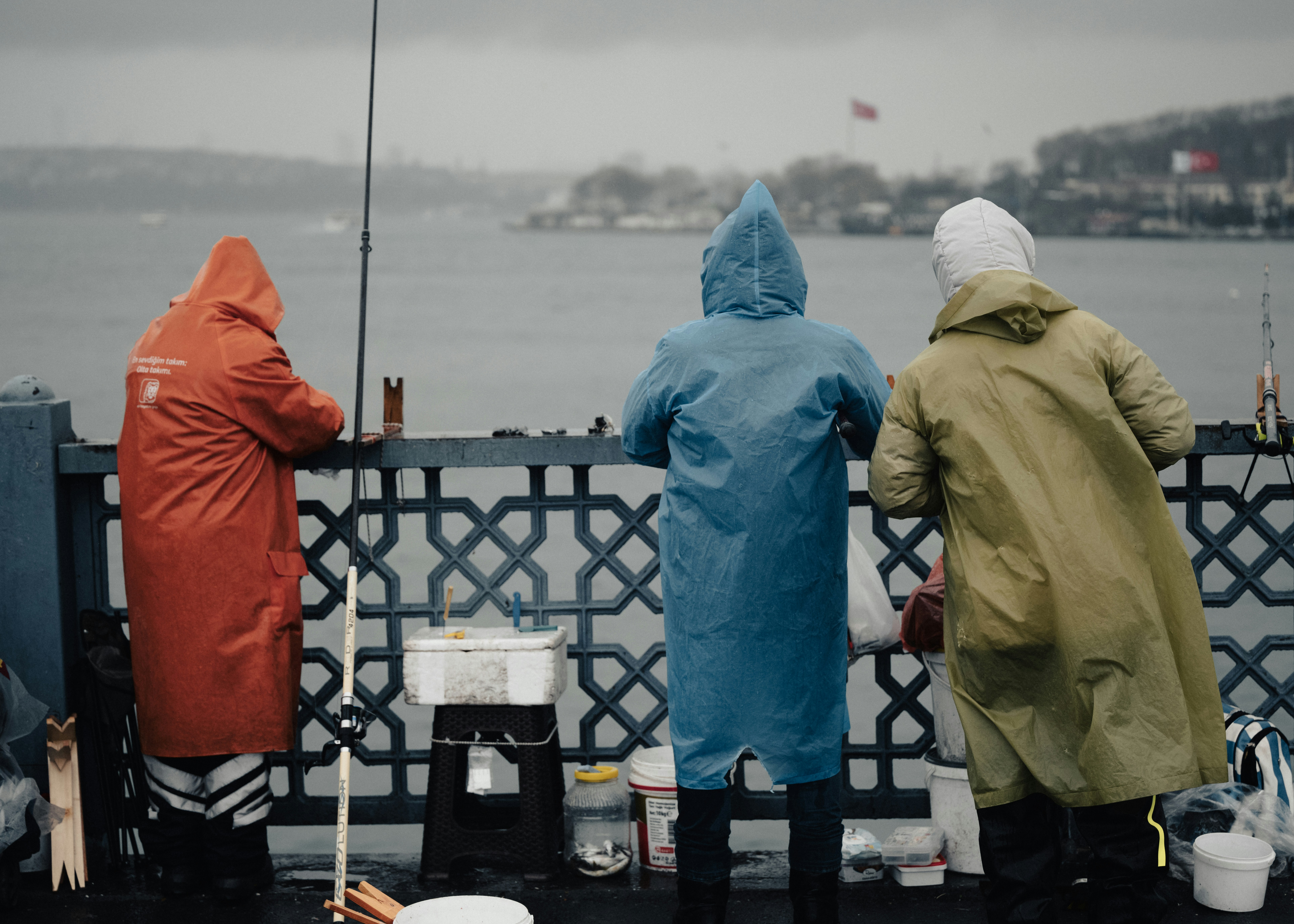Three Hooded Anglers on a Railing Watching the Sea