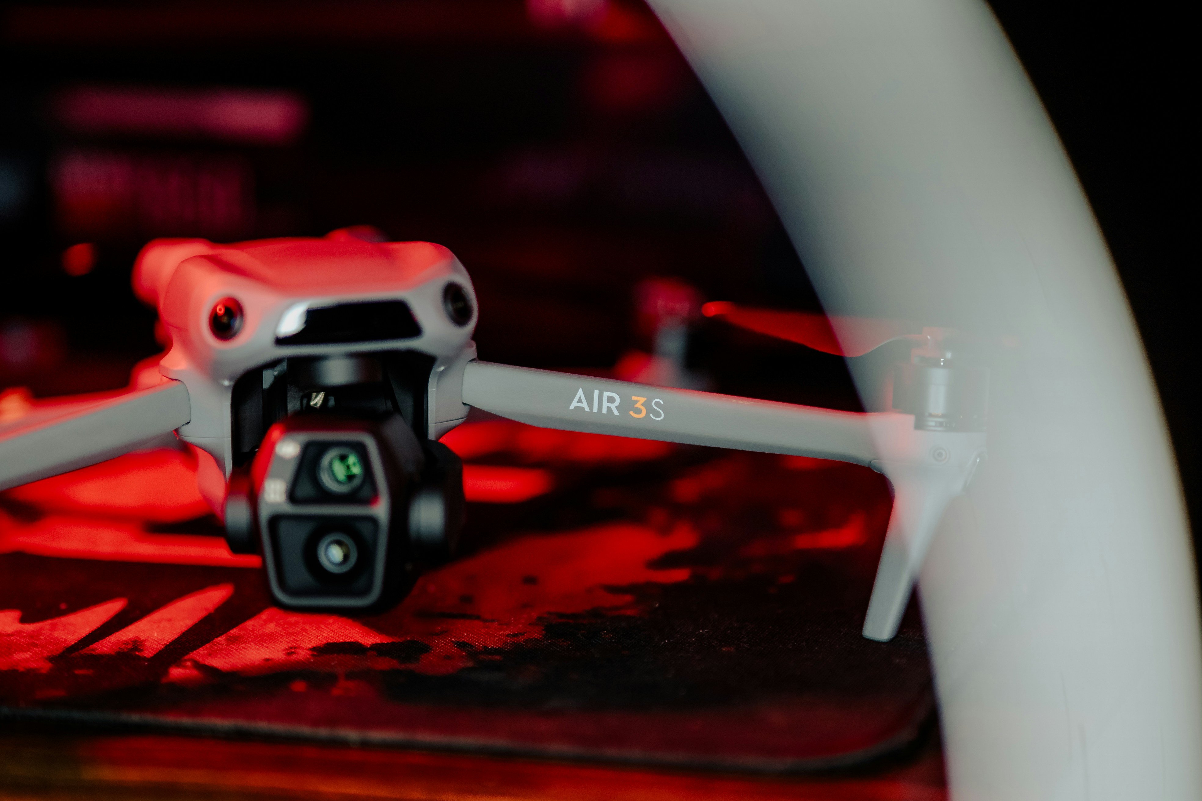 Drone model AIR 3S positioned on a textured surface, illuminated by red lighting, showcasing its sleek design and advanced camera features.