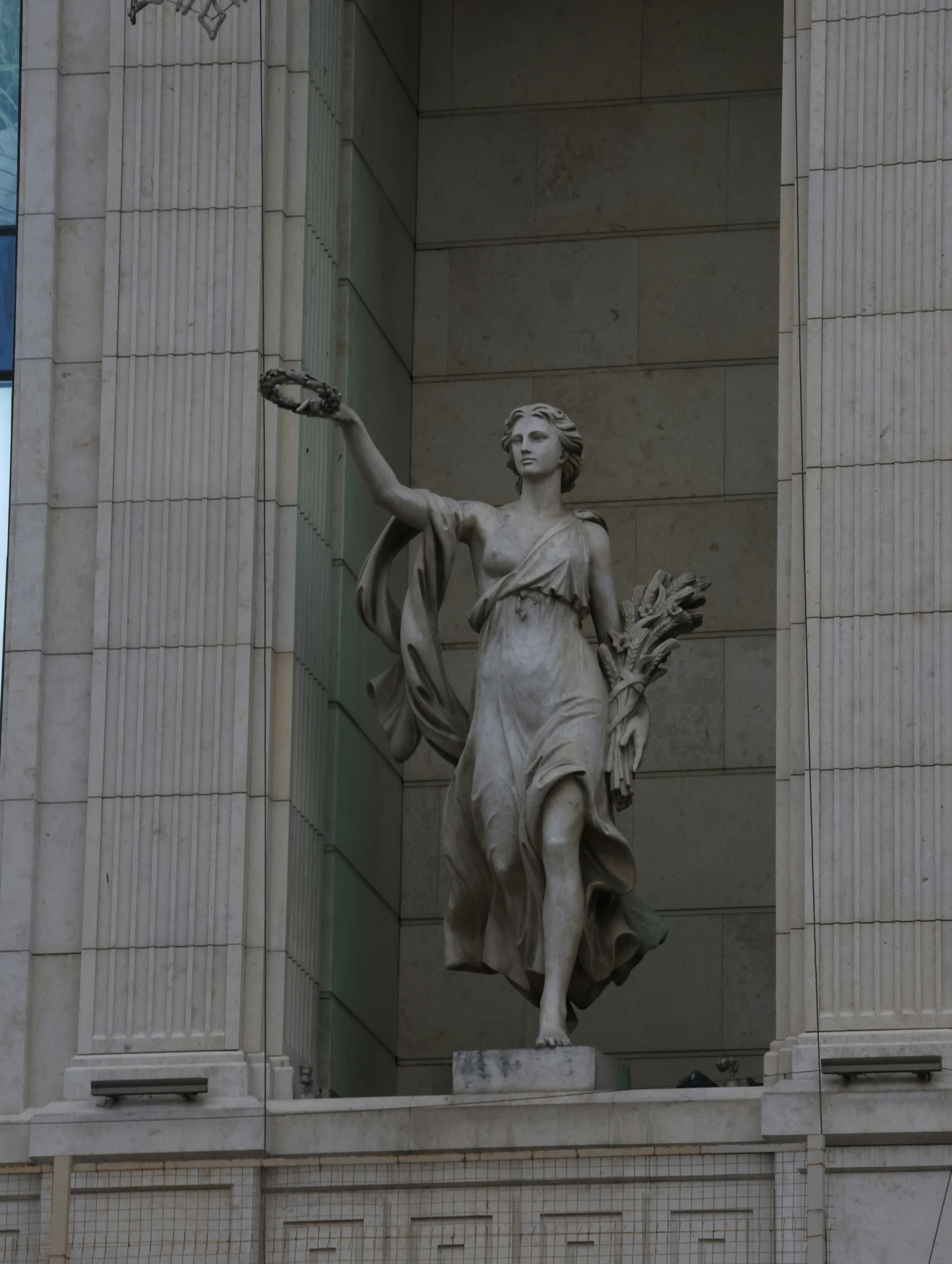 Elegant statue of a woman holding a laurel wreath, symbolizing victory and honor, set against a grand architectural backdrop.