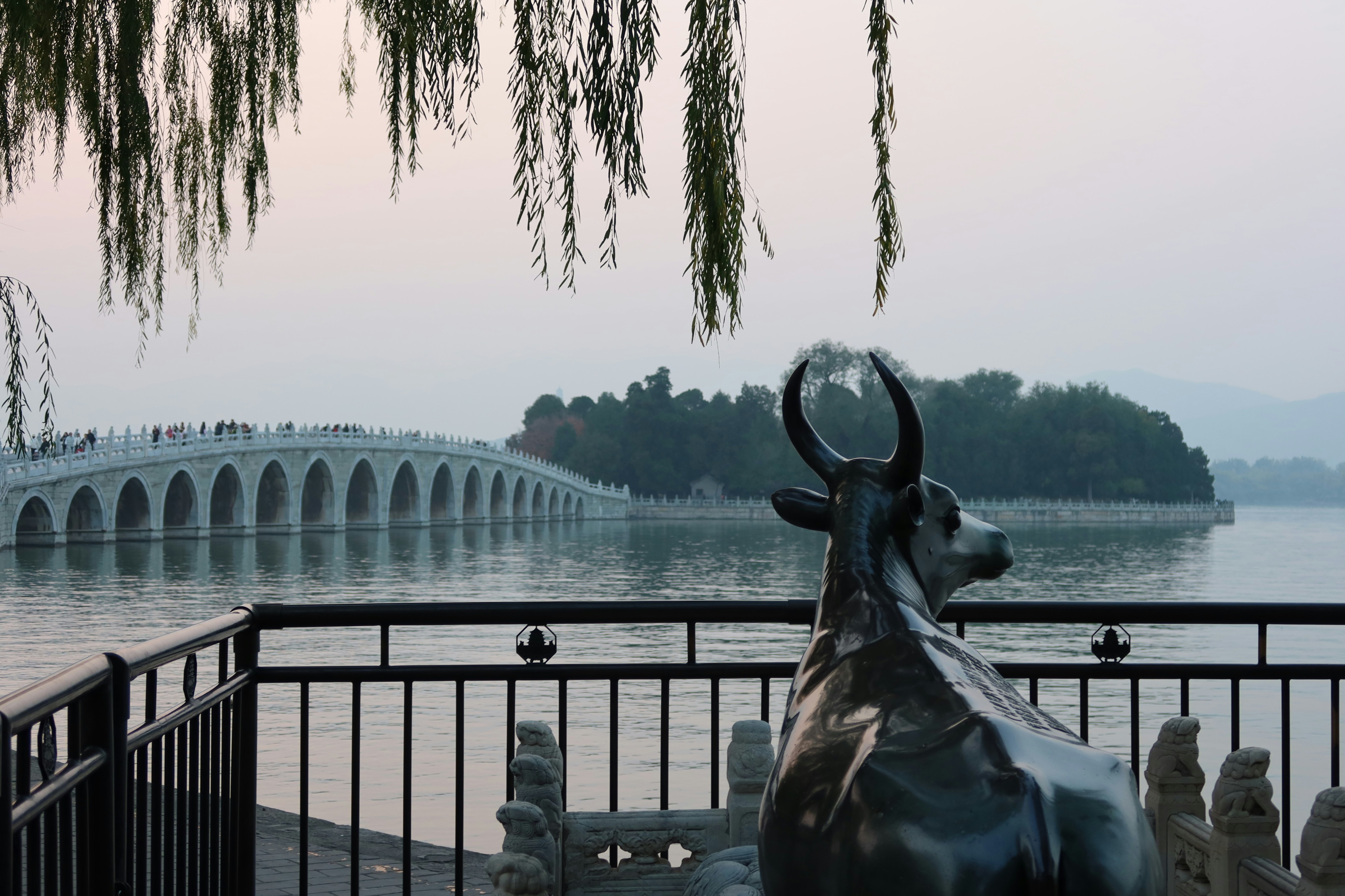 A statue of a bull on a bridge overlooking a body of water
